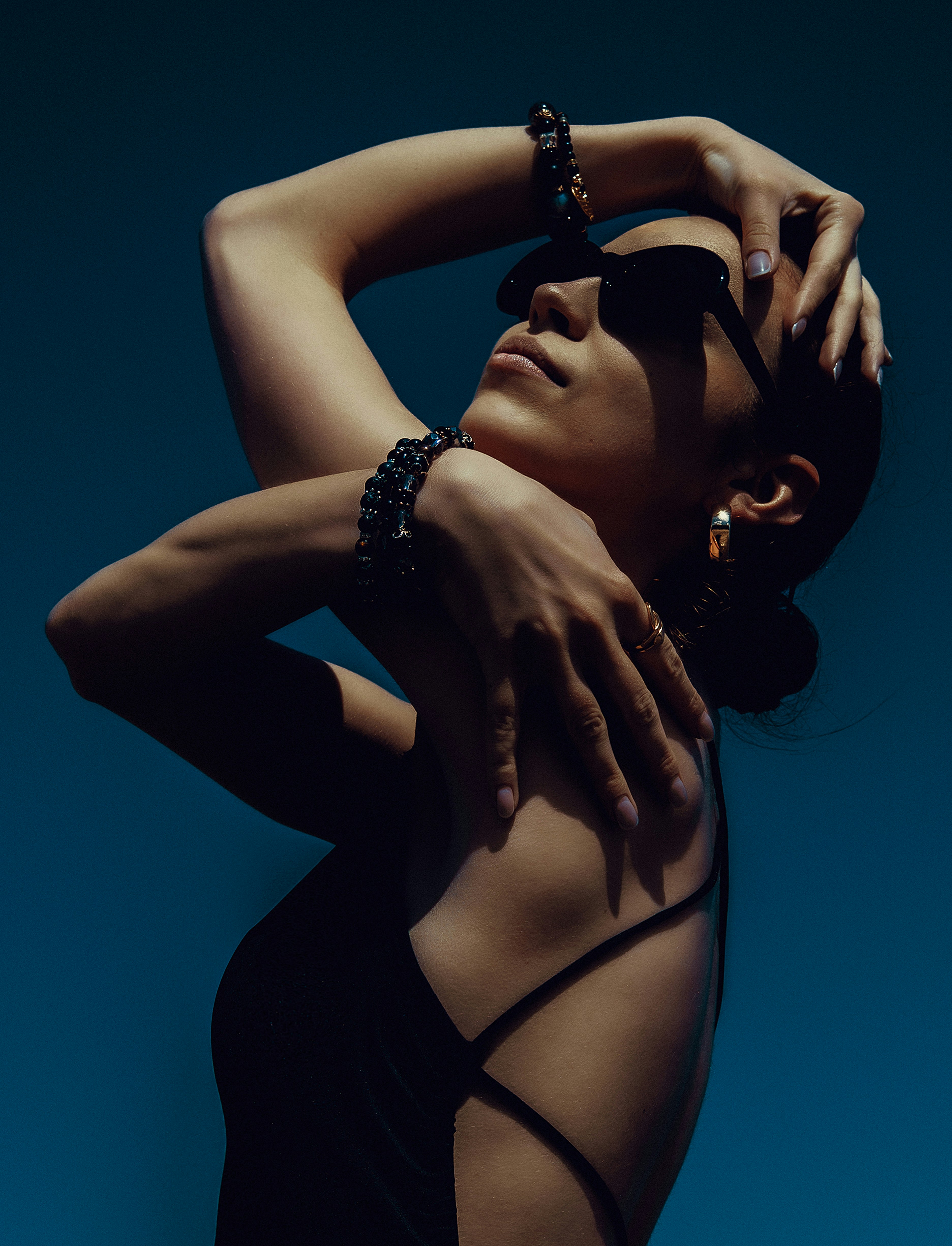 Stylish woman in sunglasses and jewelry against a vibrant blue.