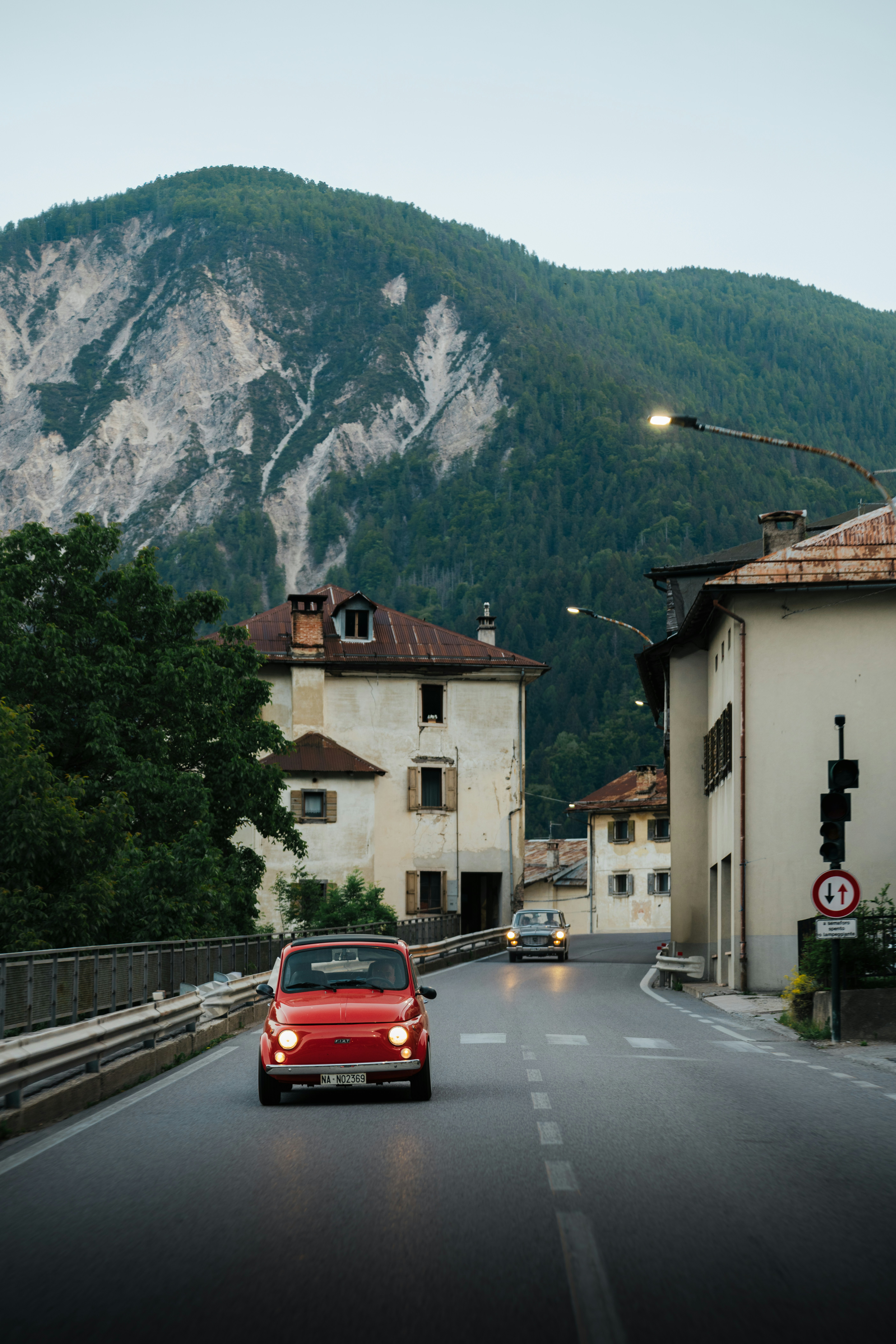 Red Coupe on a Mountain Pass Under a Skyscraping Village