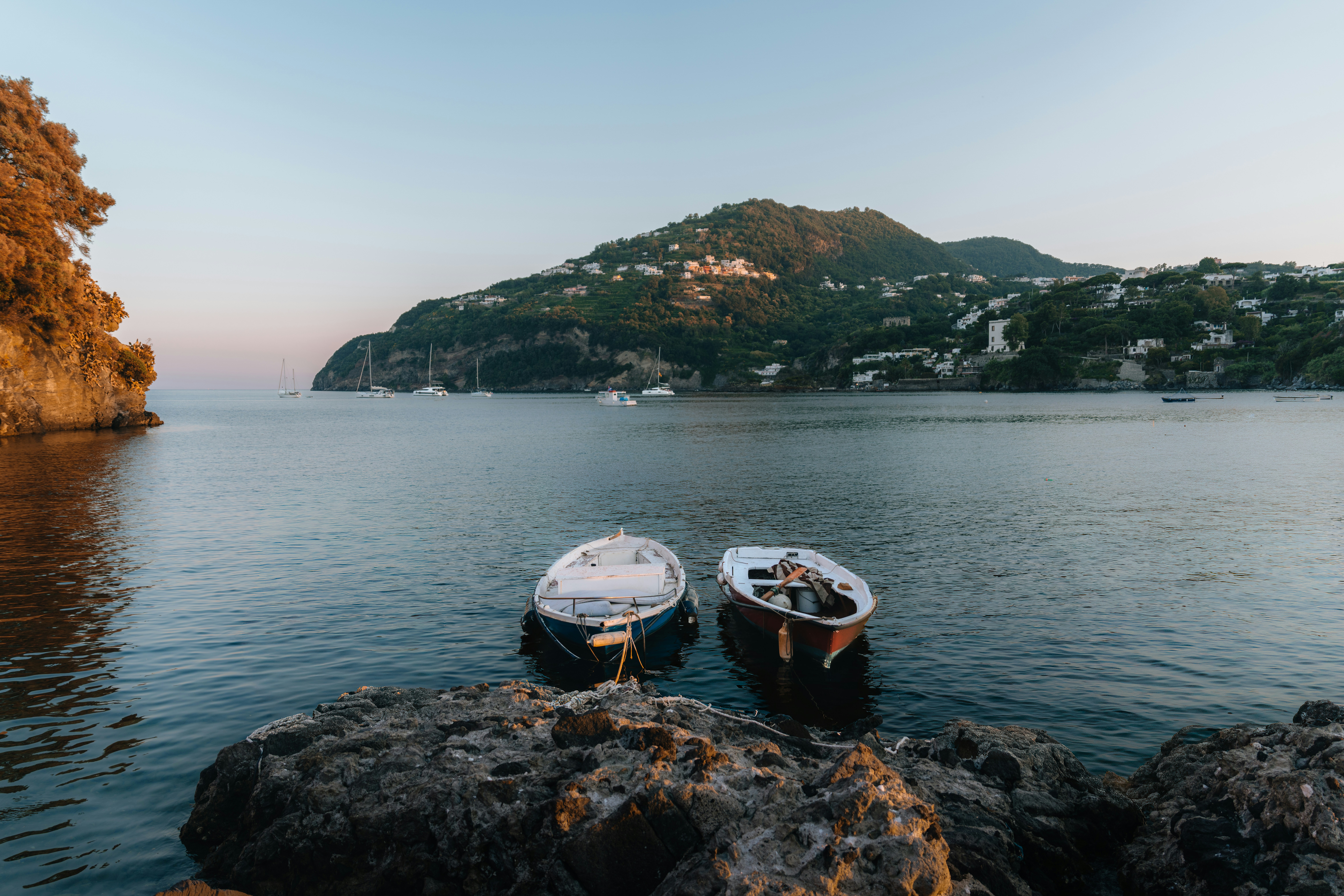 Two small boats float in a calm bay at sunset.