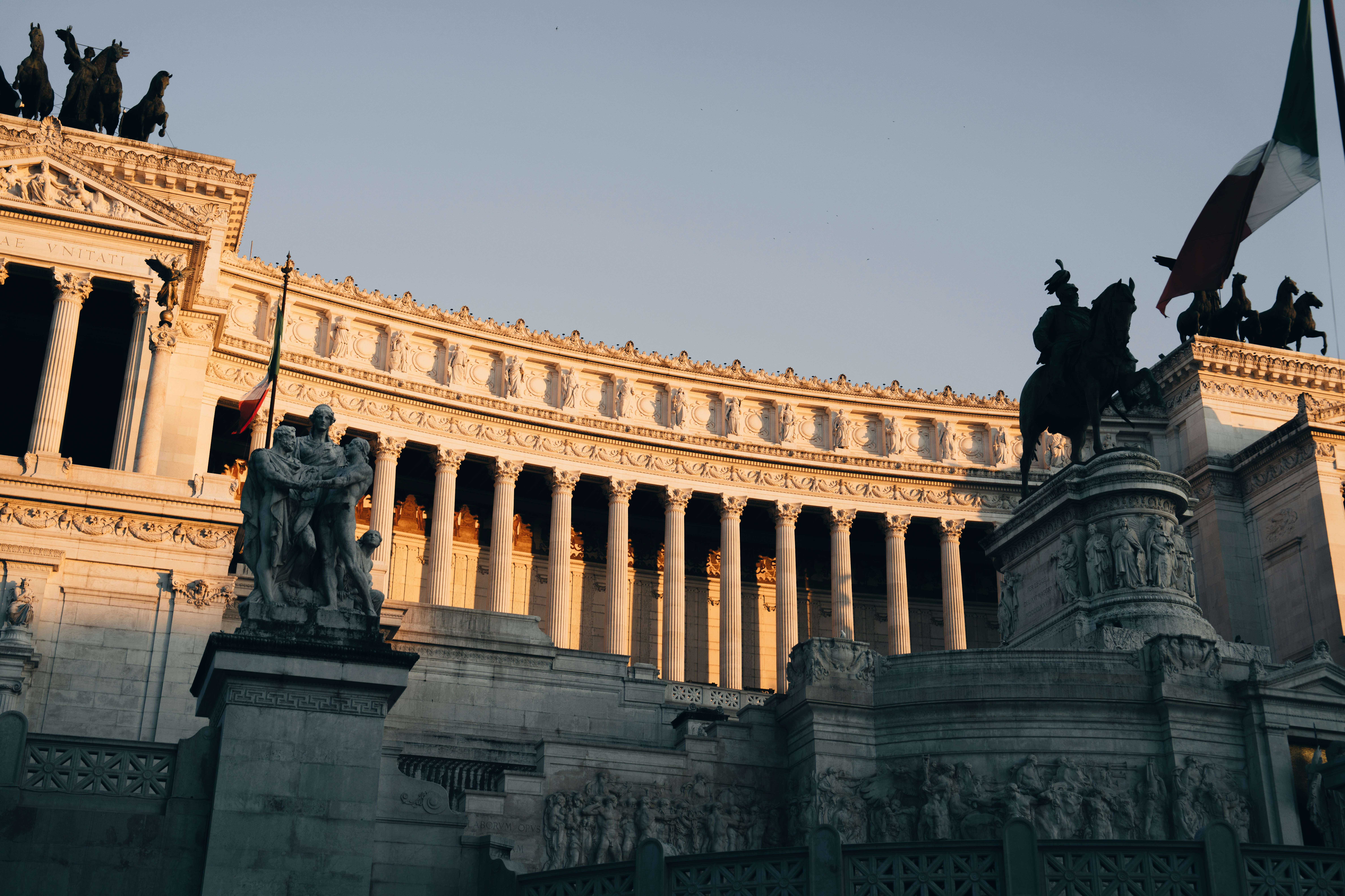 Historic roman monument with statues and flags at sunset.
