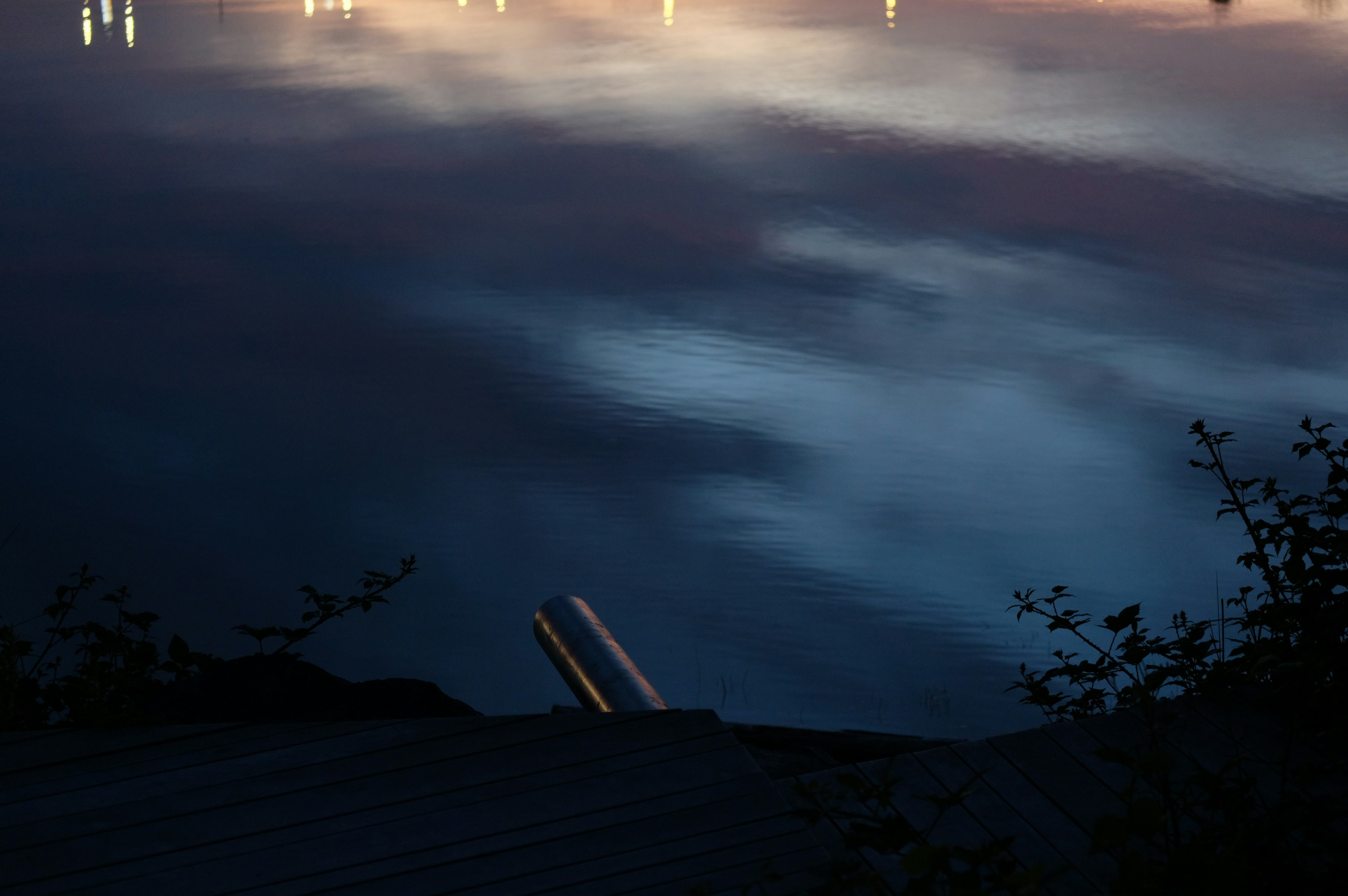 Dim Shoreline Echo: A lone metallic cylinder at the water’s edge under a moody dusk