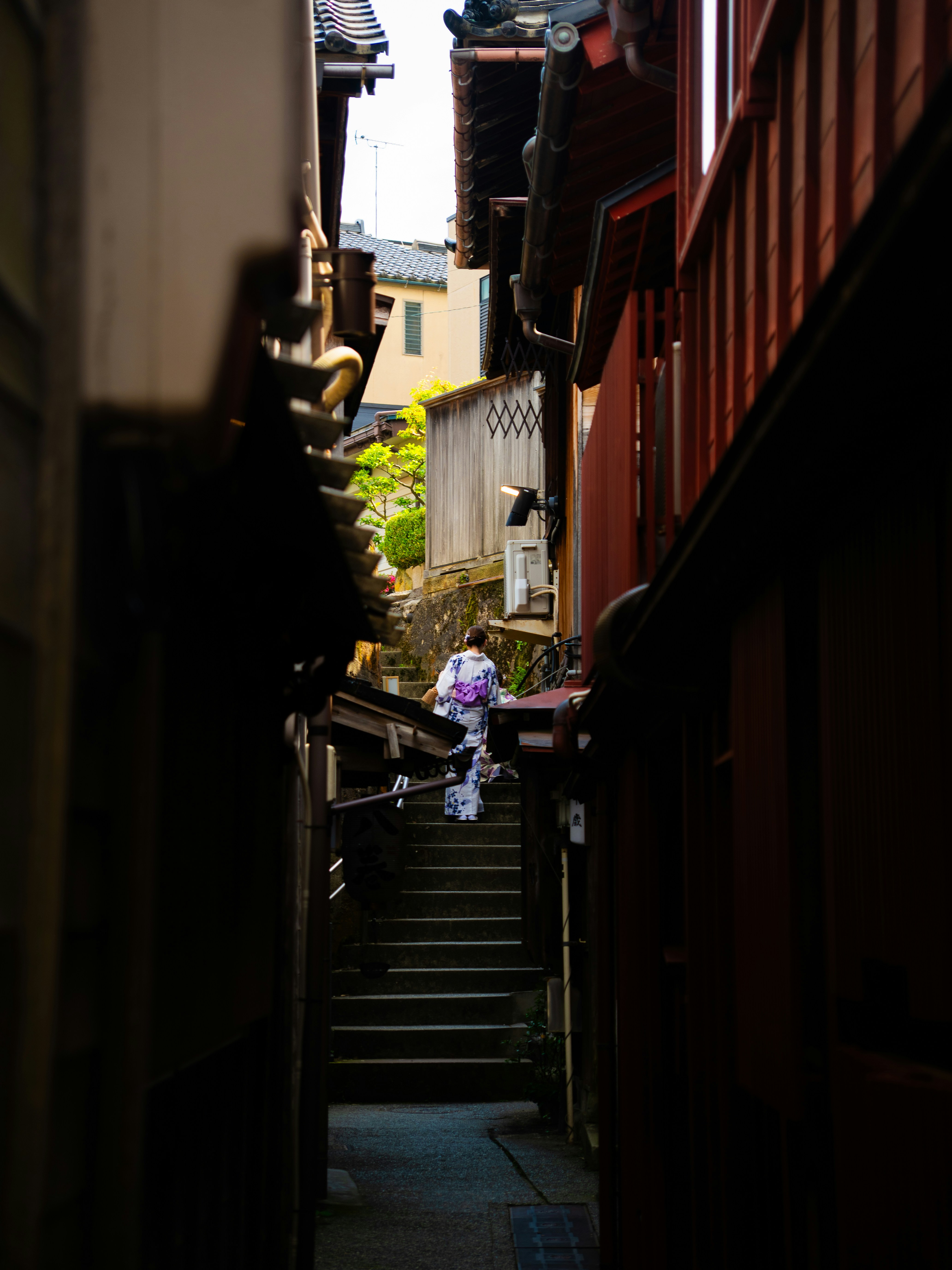 Narrow traditional japanese alley with a person ascending stairs.