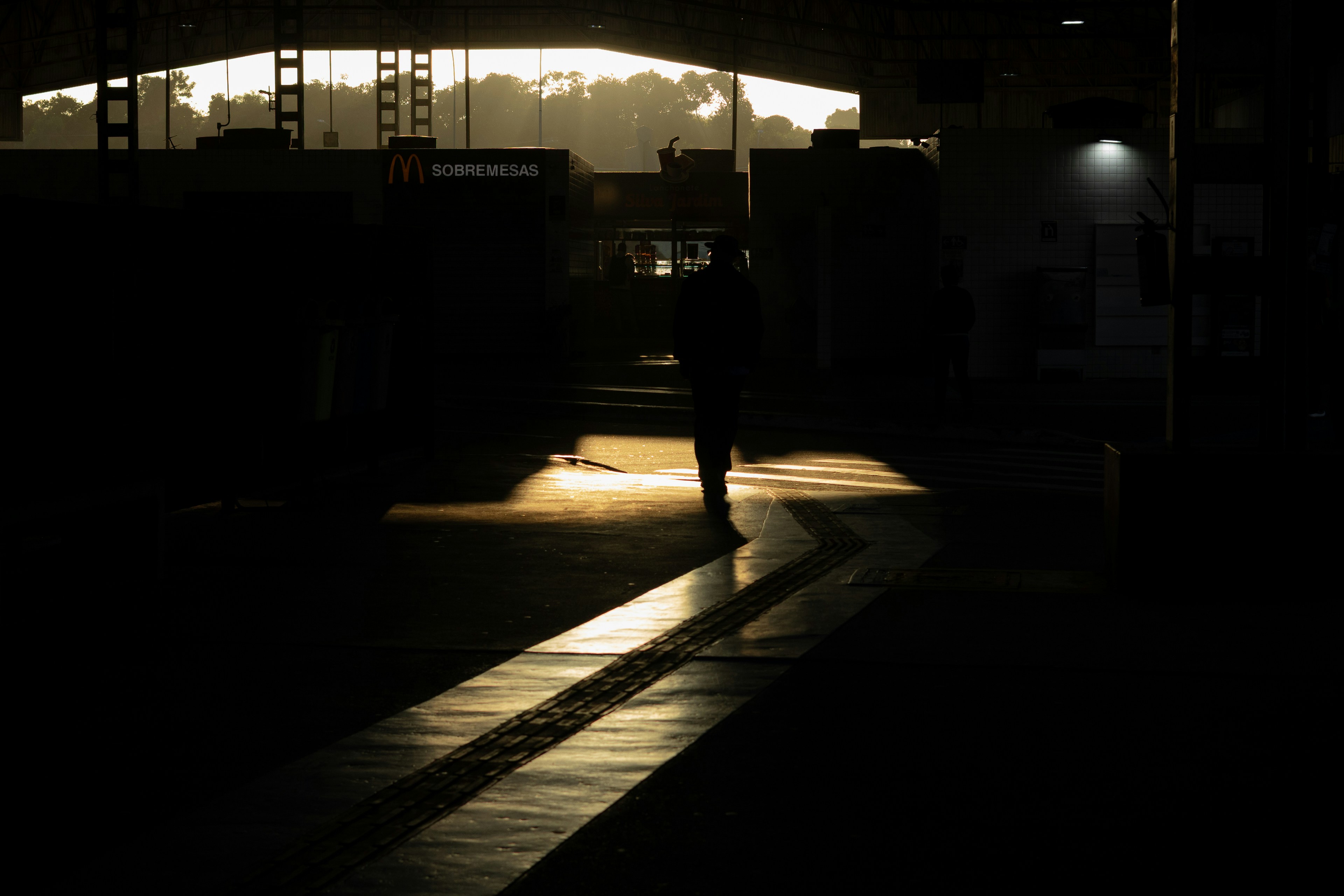 Guiding Light: a lone figure steps into a channel of gold on a dim station floor