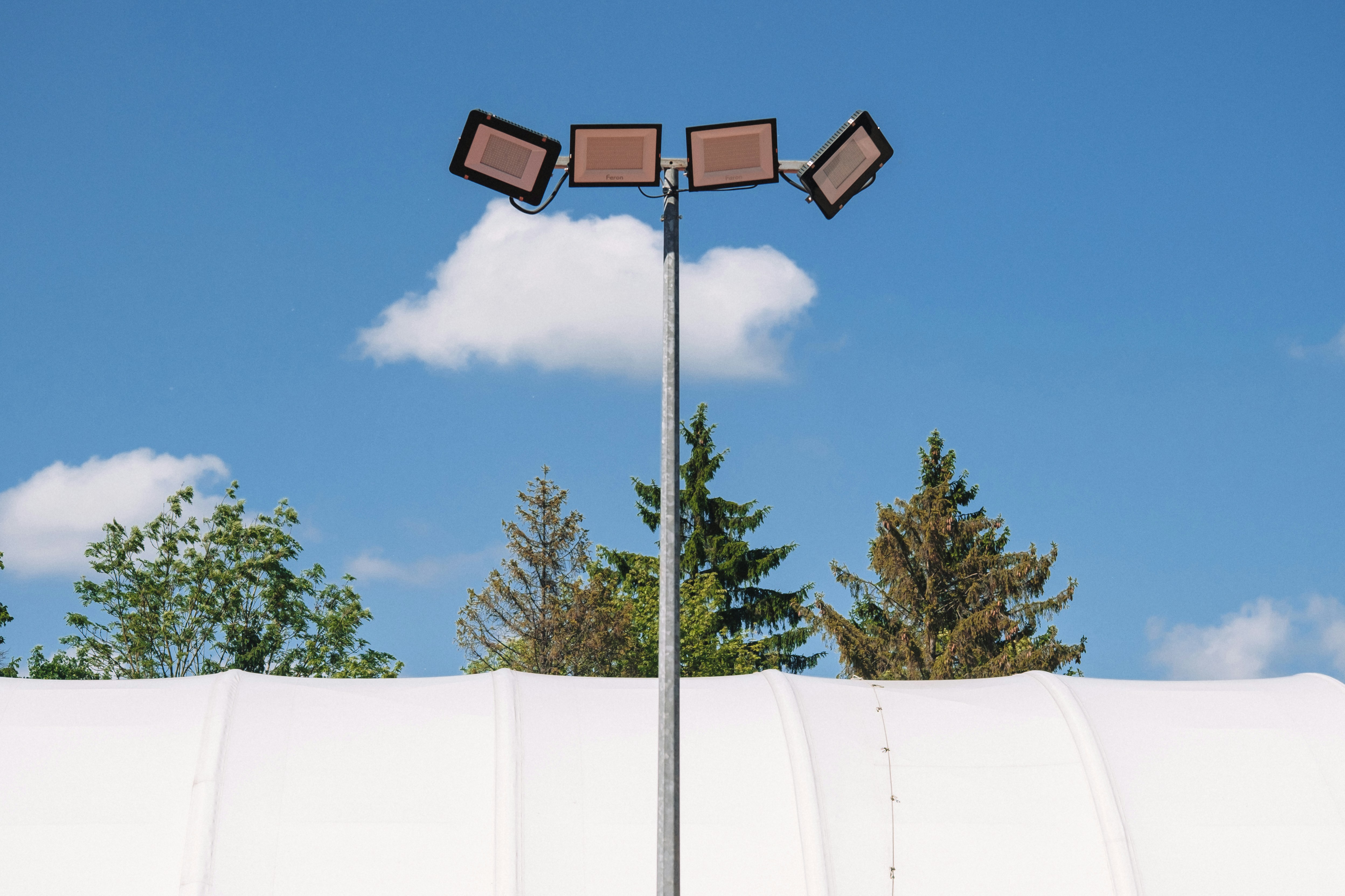 Four floodlights on a pole against a clear blue sky.