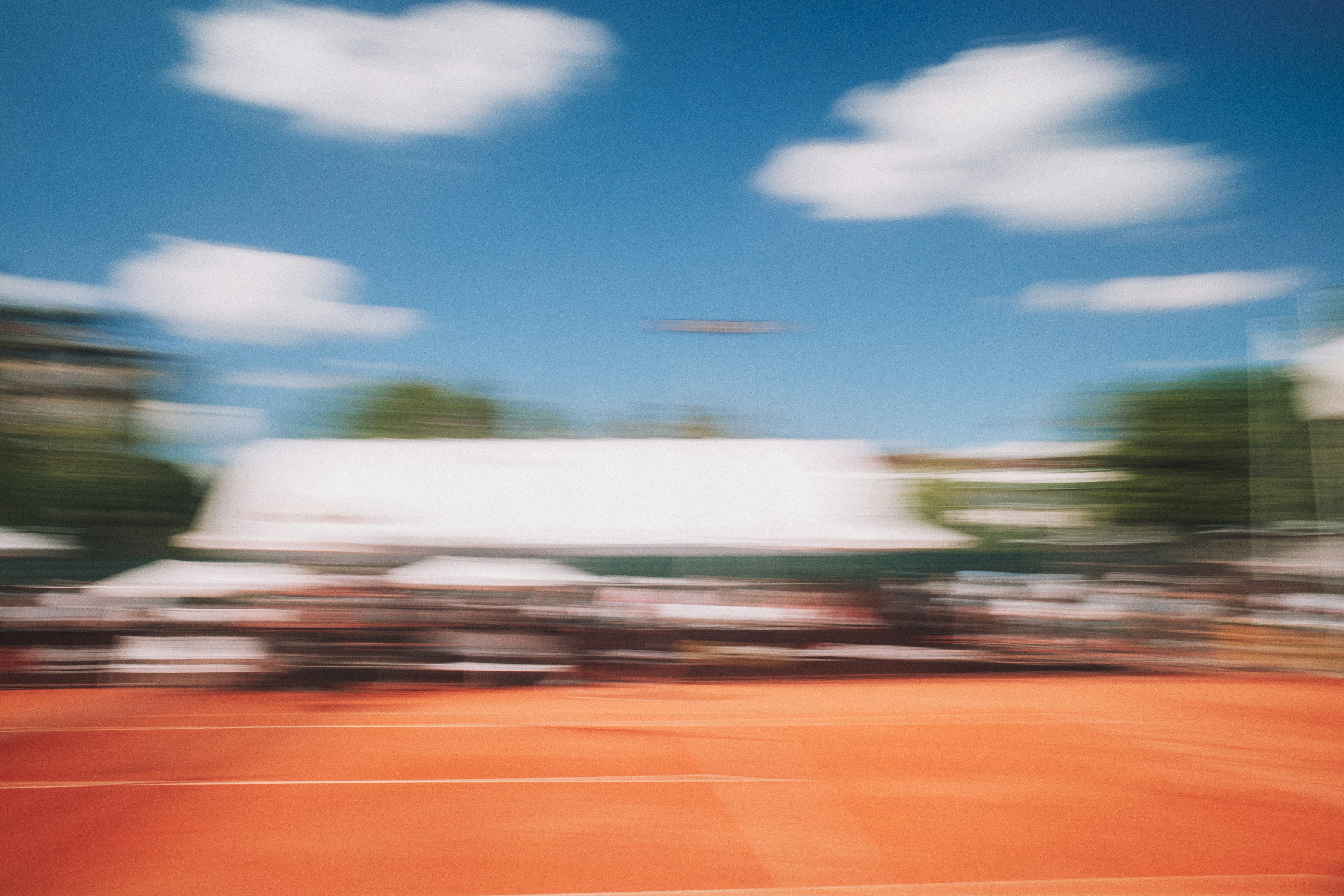 Blurry tennis court under a blue sky with white clouds.