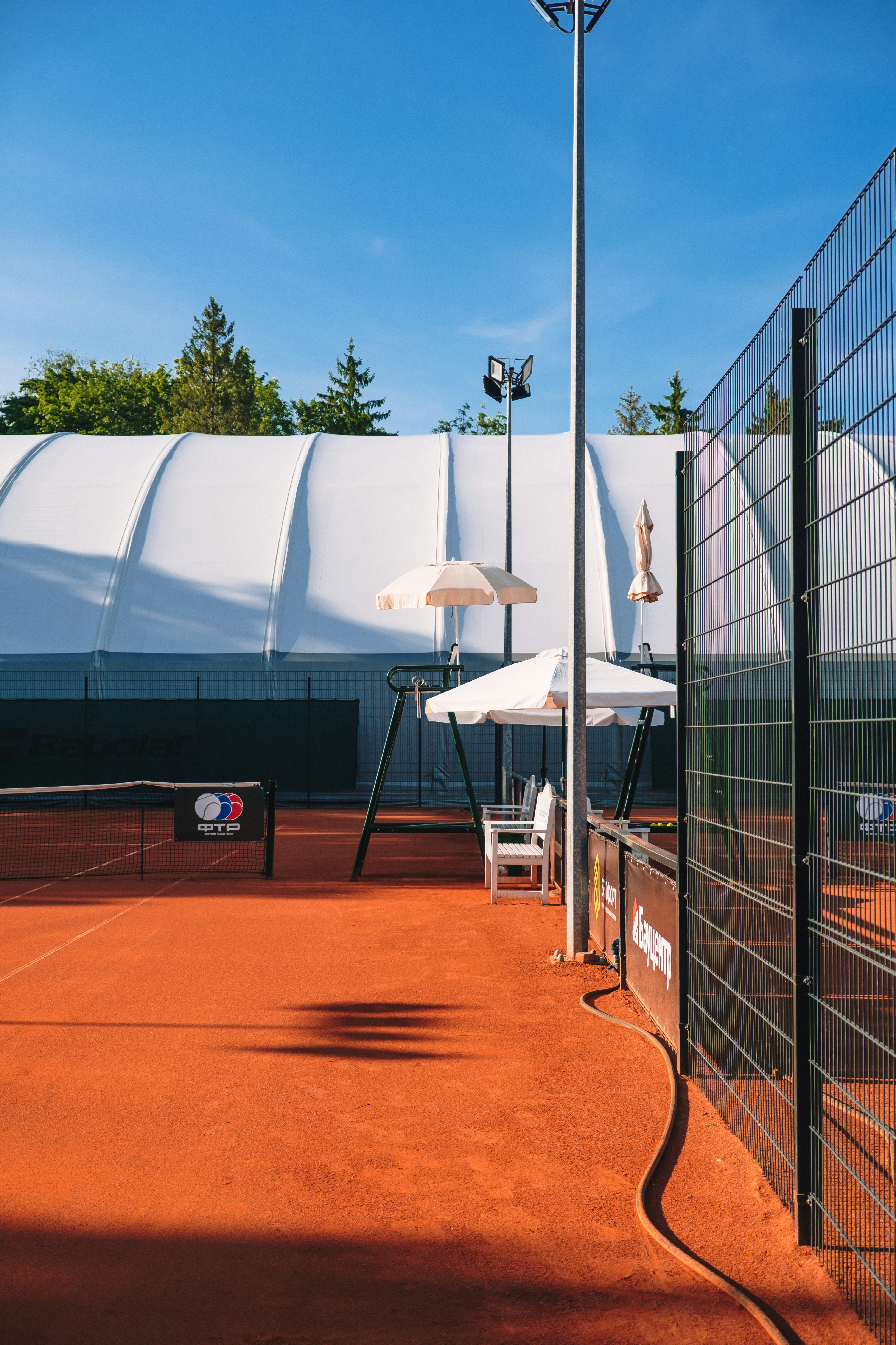 Sunlit Tennis Court with Protective Dome and Side Fence