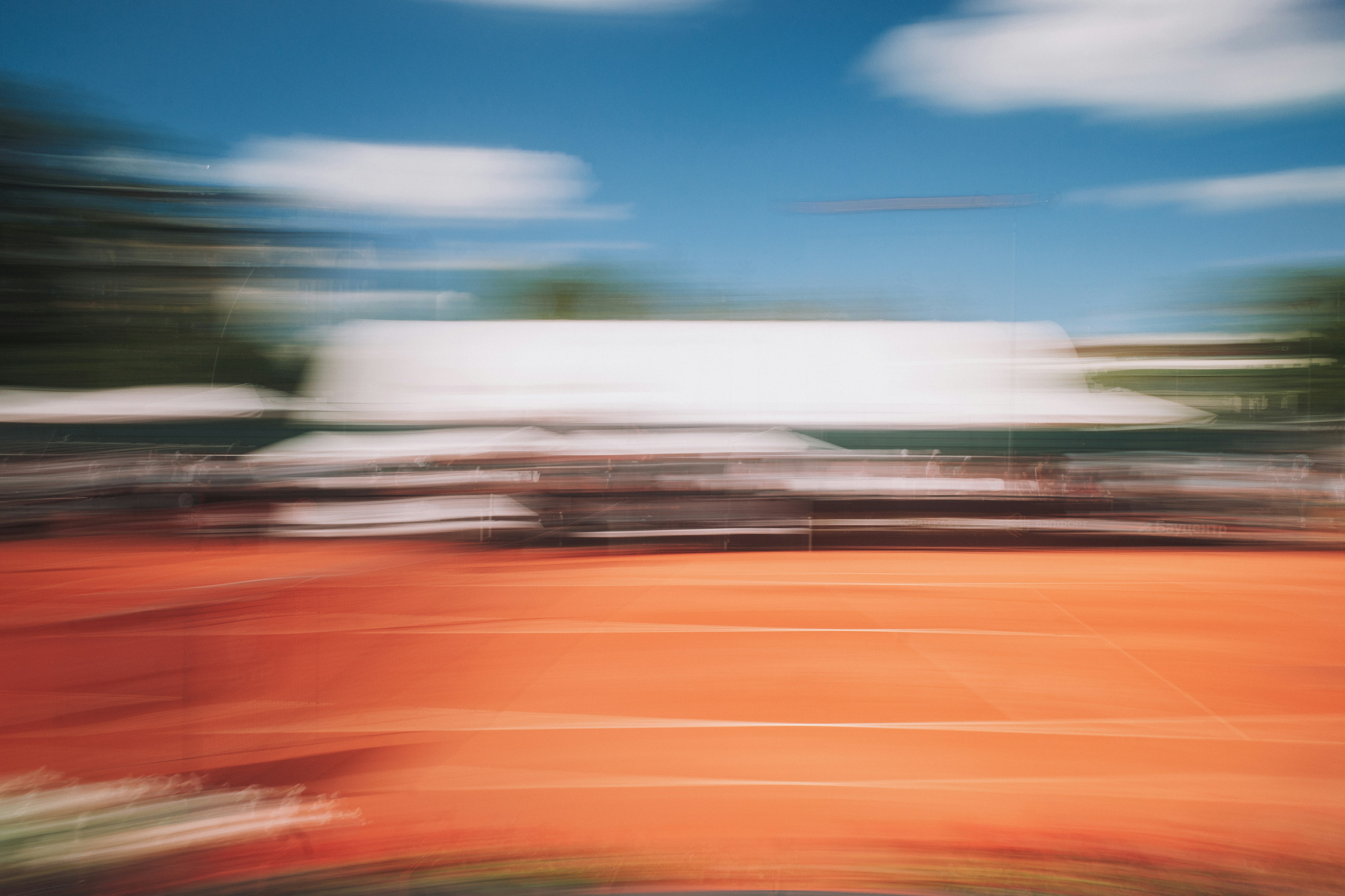 Blurry clay tennis court with white structure and blue sky.