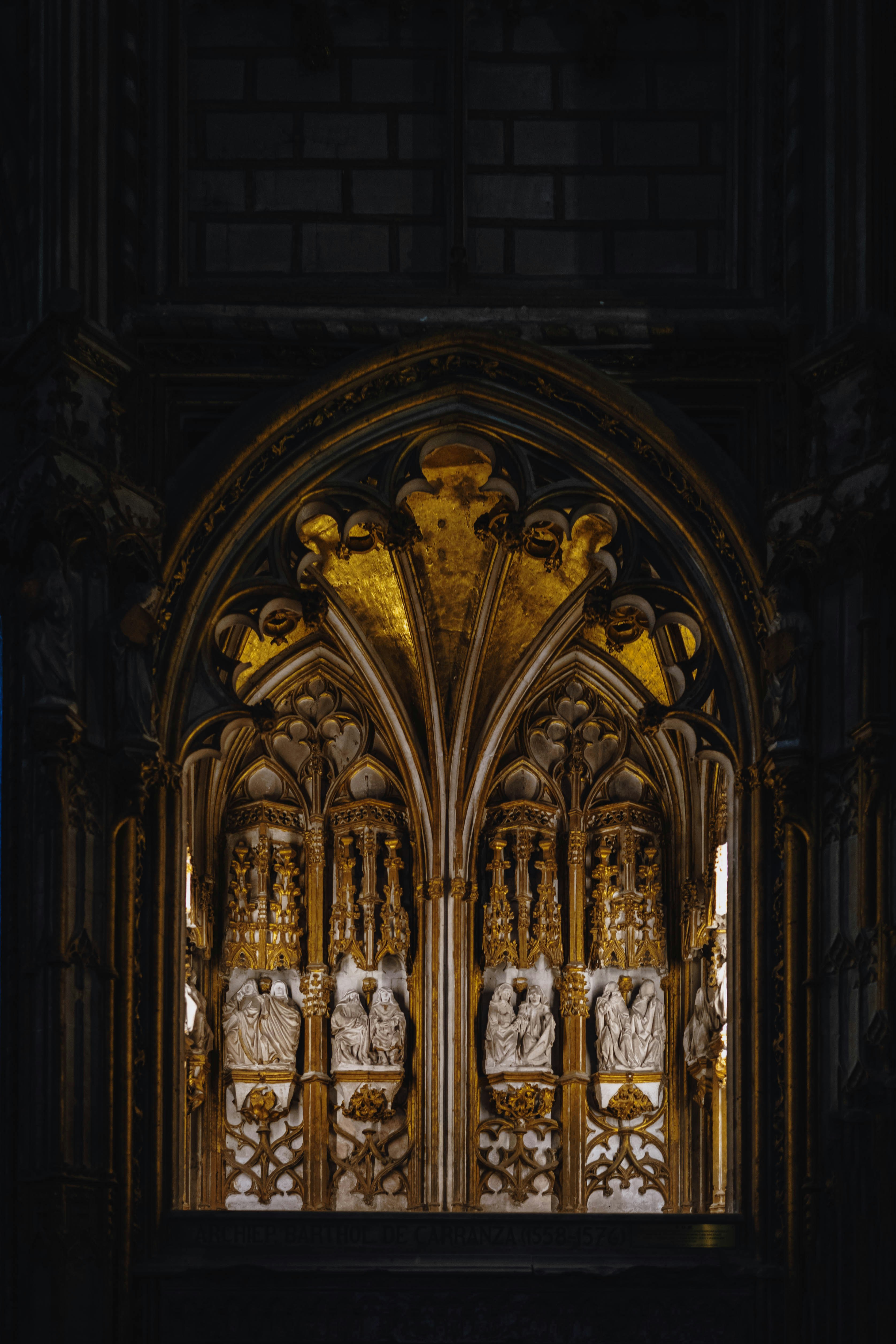Ornate golden and white gothic window in a dark interior.