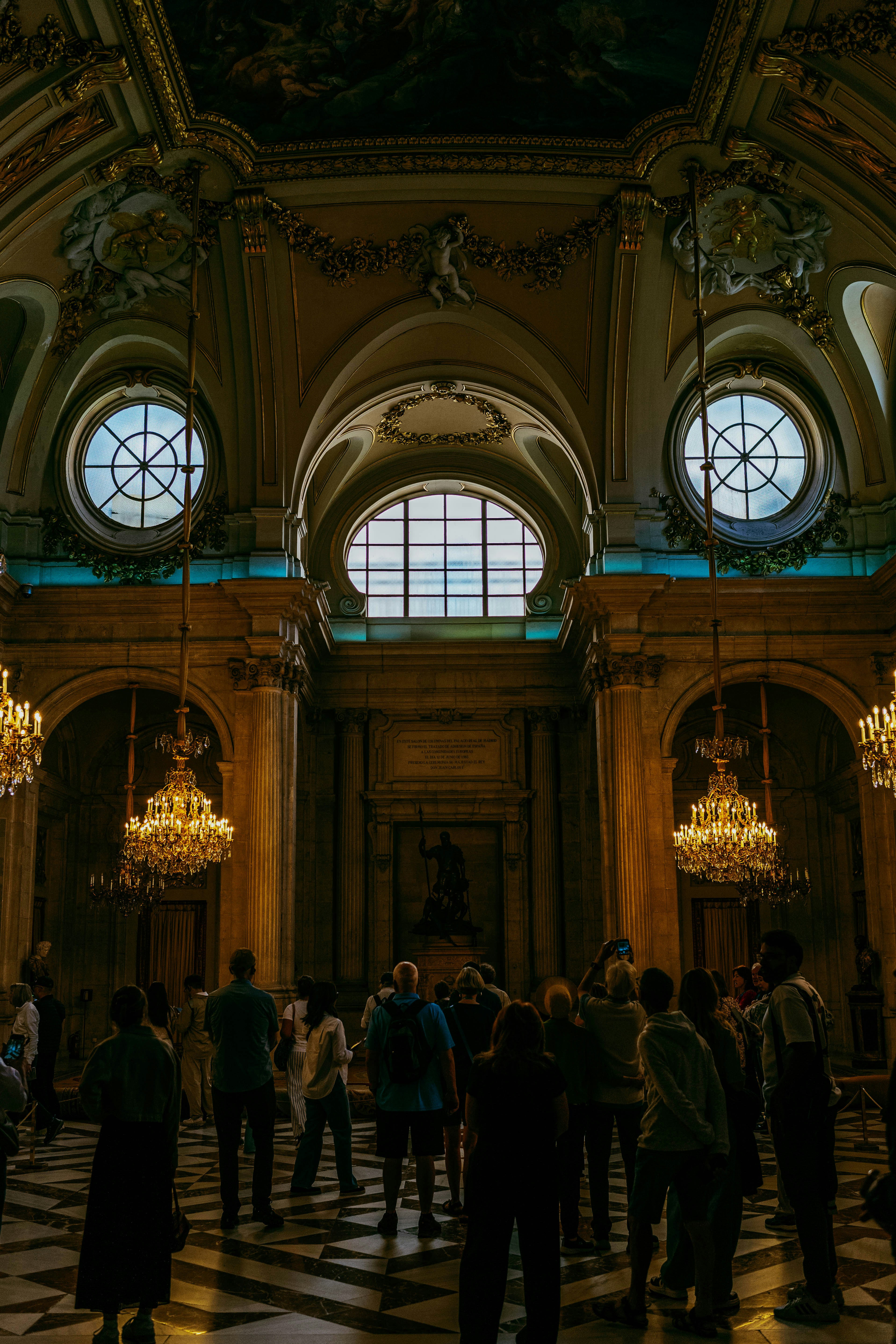 Visitors in a majestic hall with ornate decor and chandeliers.