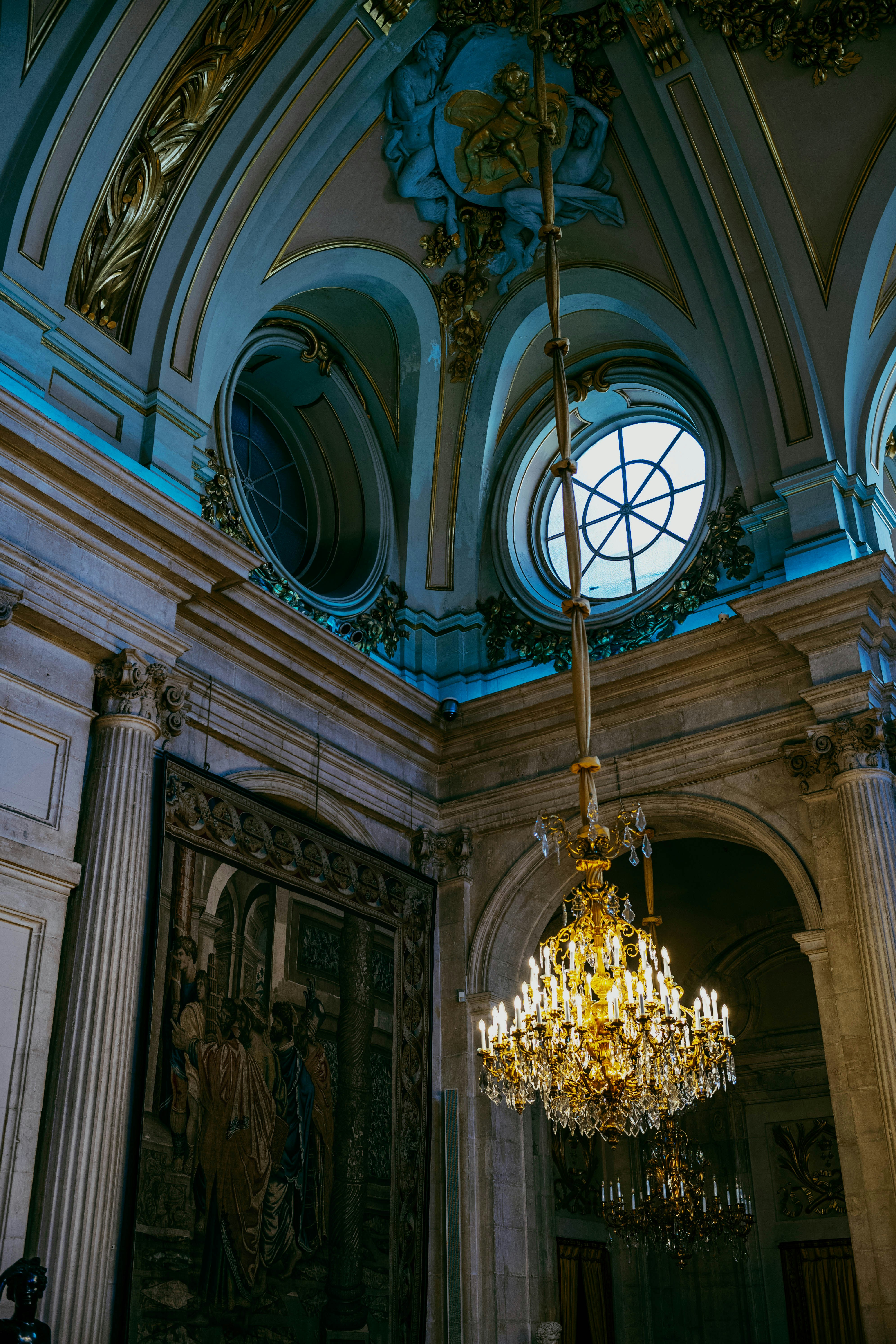 Grand hall with ornate ceiling, tapestry, and crystal chandeliers.