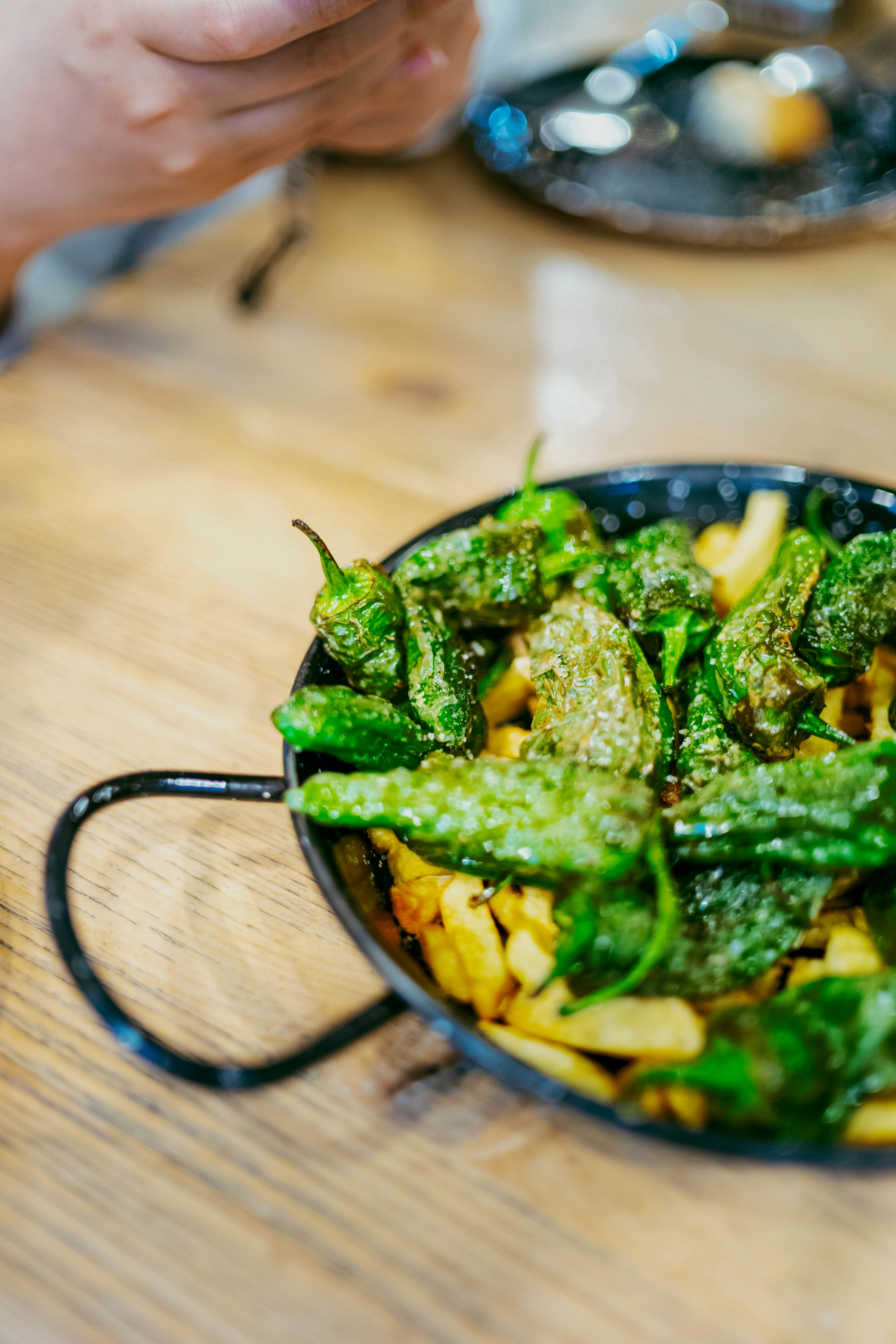 Green padrón peppers and french fries in a black pan.