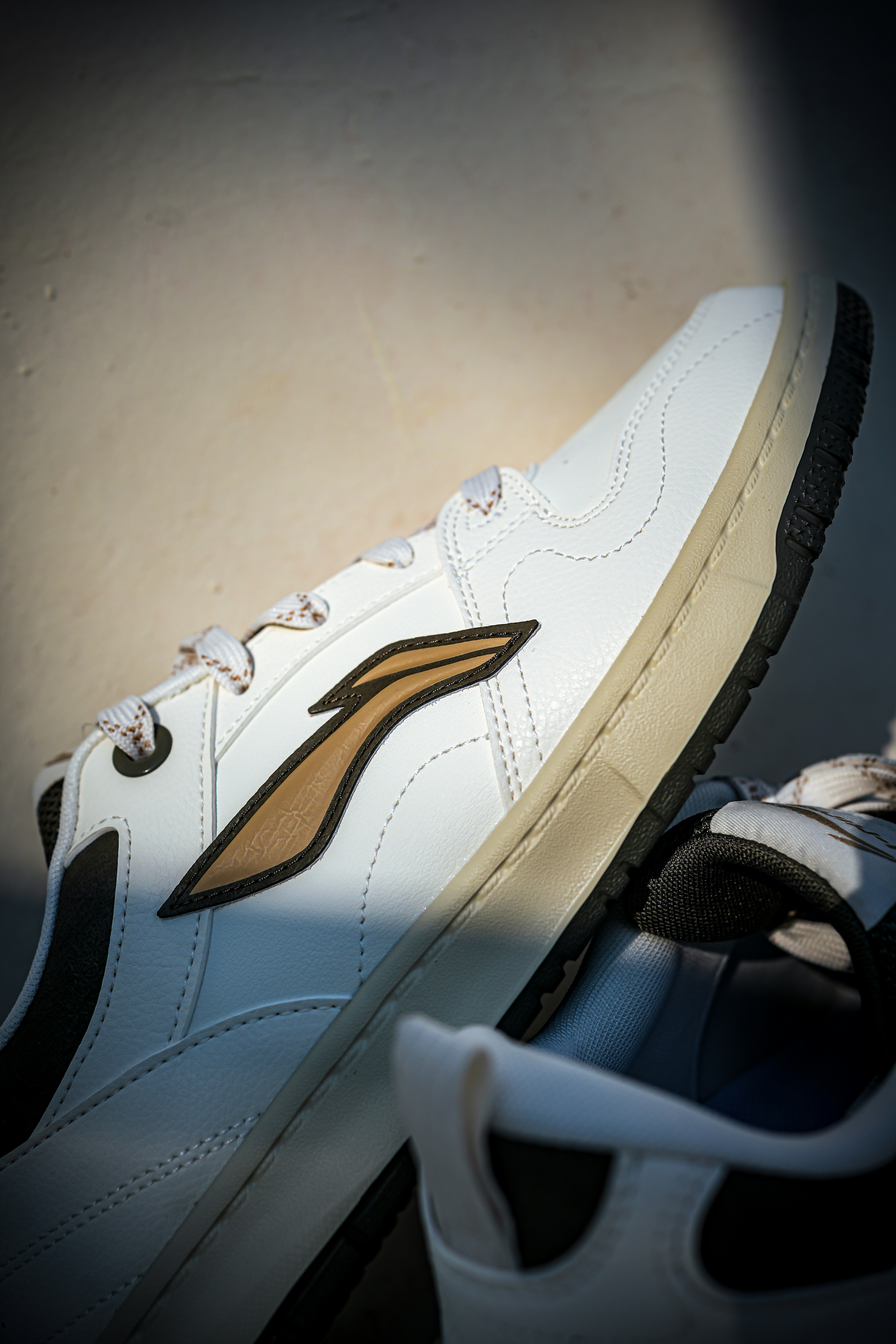 White sneaker with a tan logo rides a shadowed ground