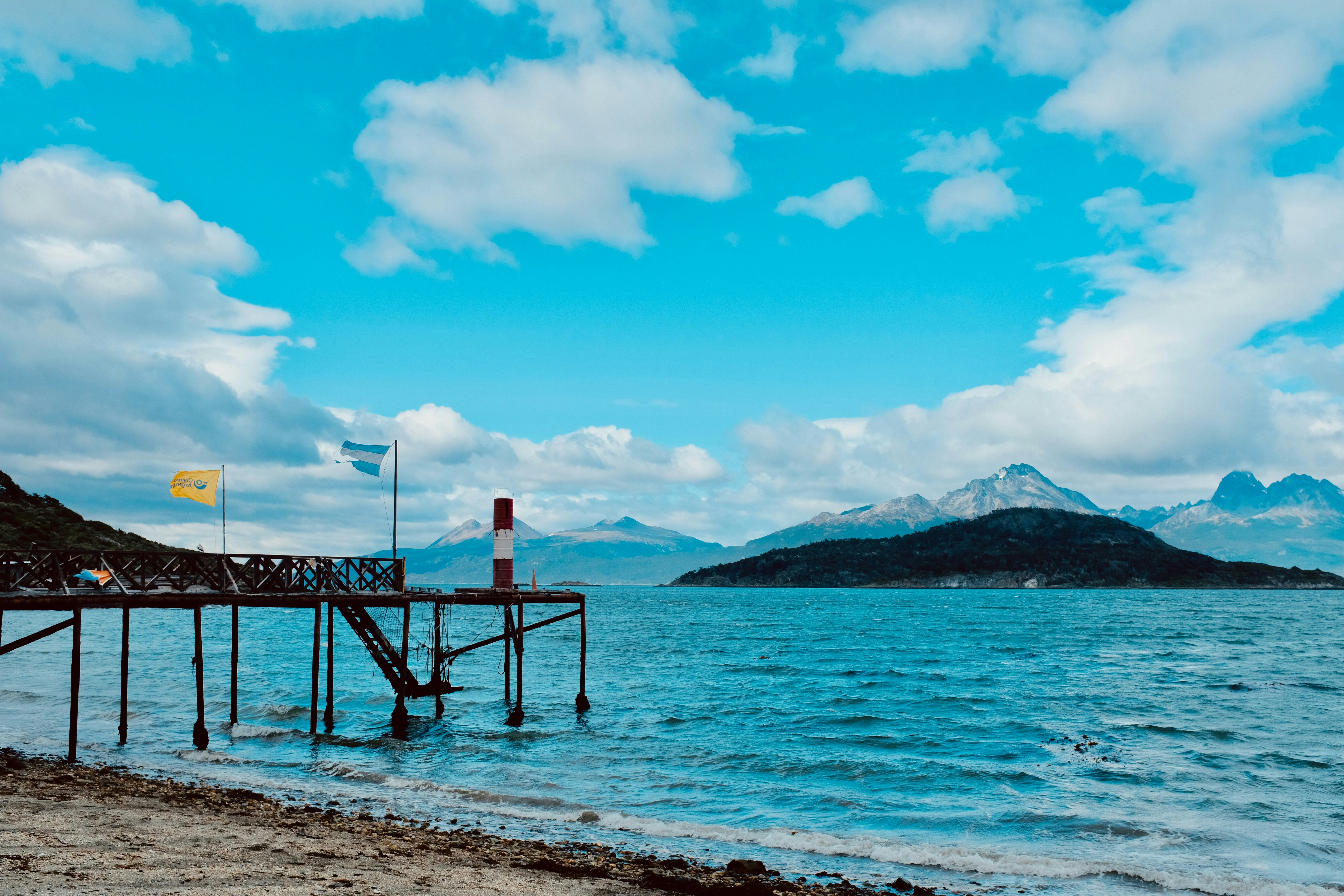Rail-head Over Blue Waters: A Quiet Pier Extends Toward Distant Mountains