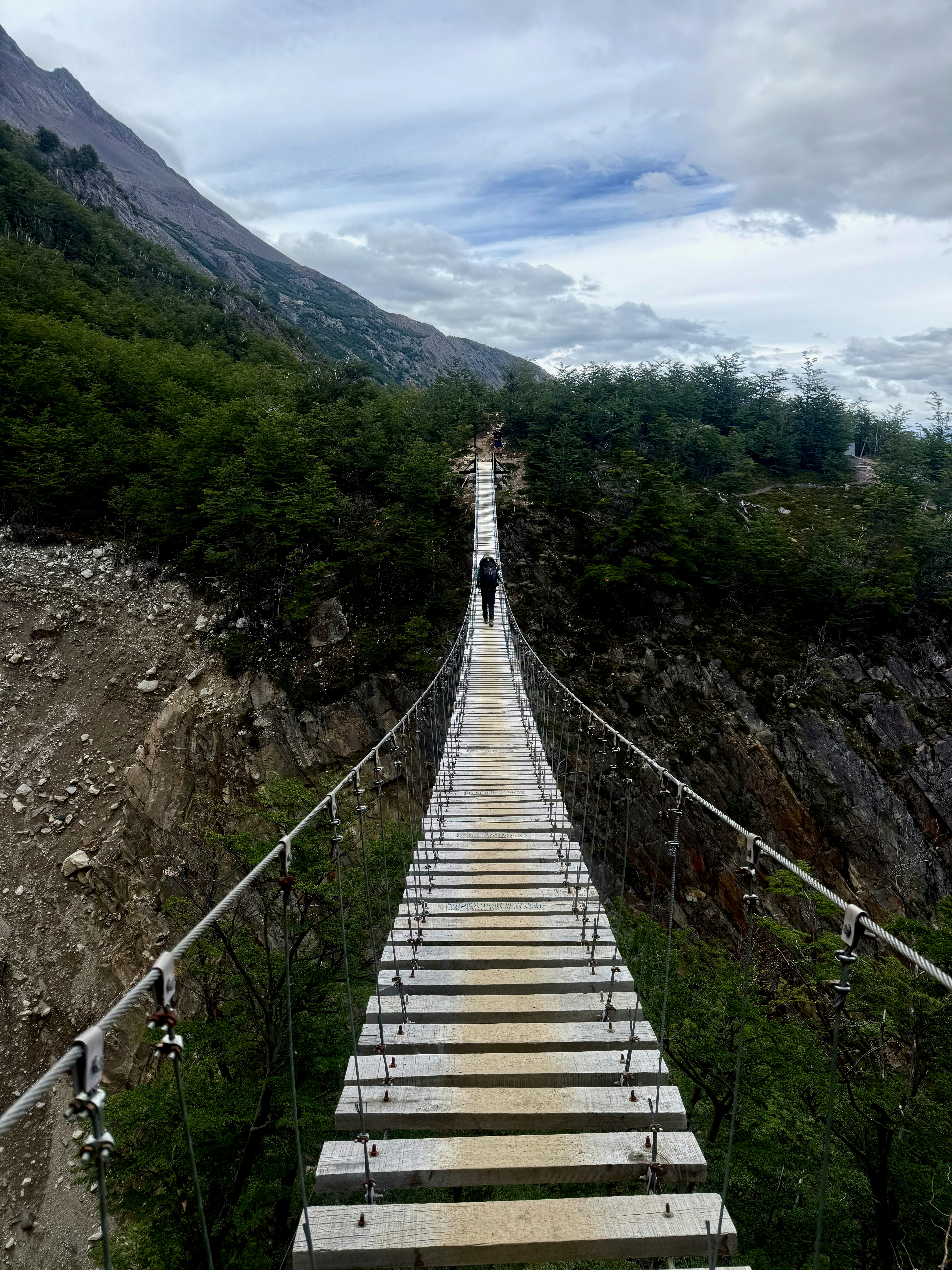 A hiker crosses a suspension bridge over a mountain valley.