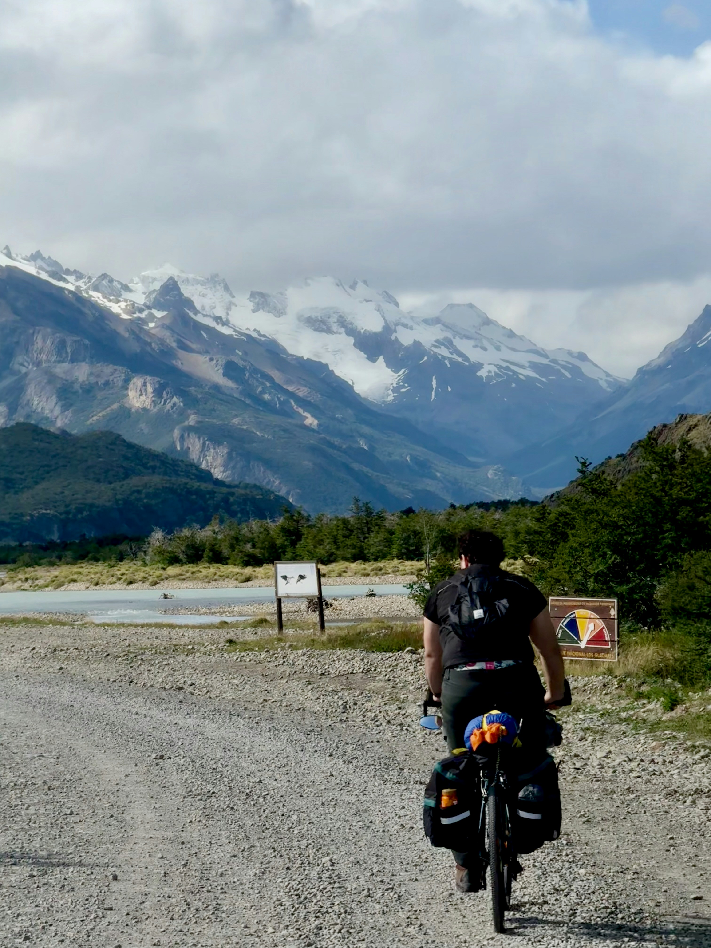 Cyclist toward distant glacier. A rugged gravel road under towering alpine peaks