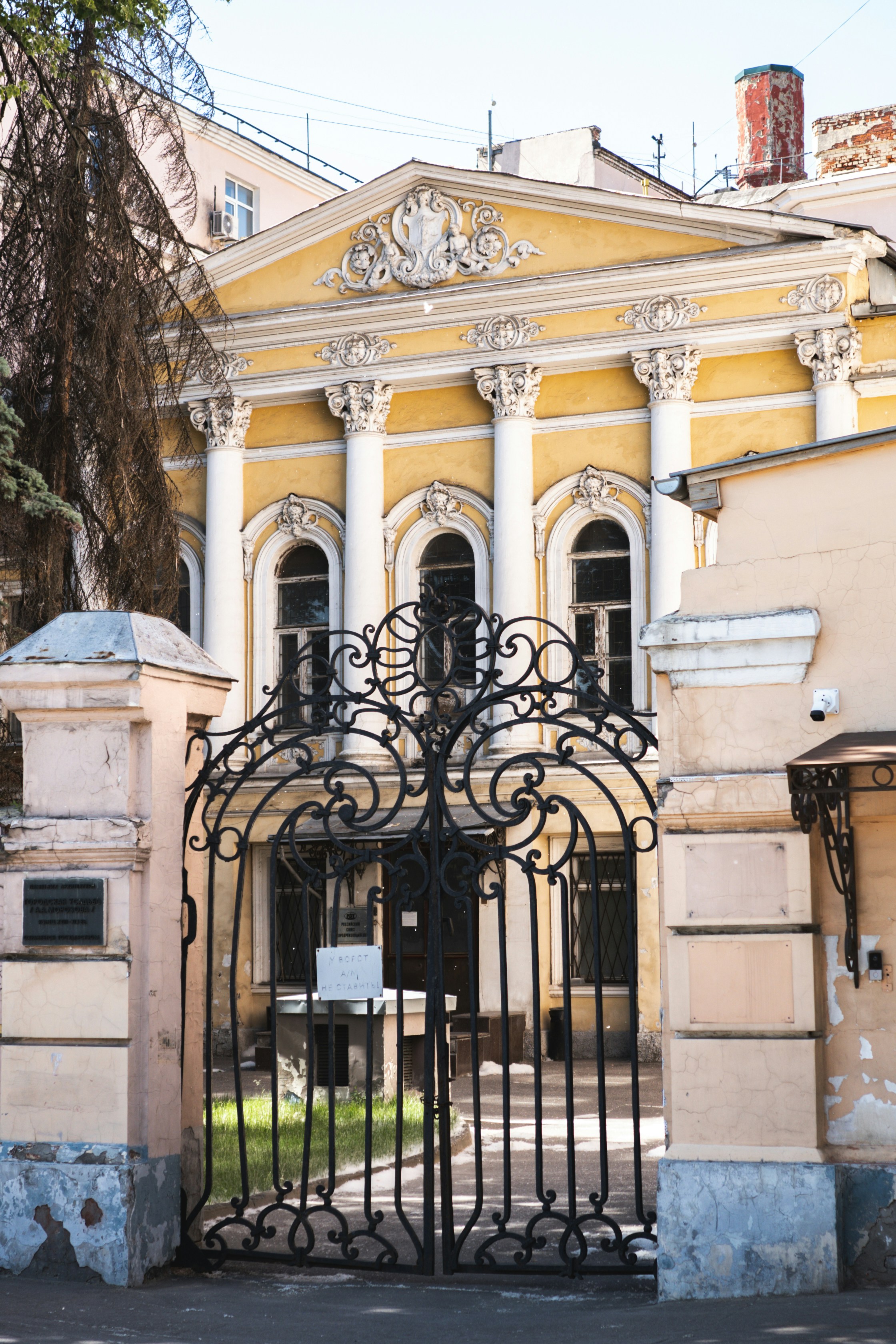 Historic yellow building with columns behind an ornate iron gate.