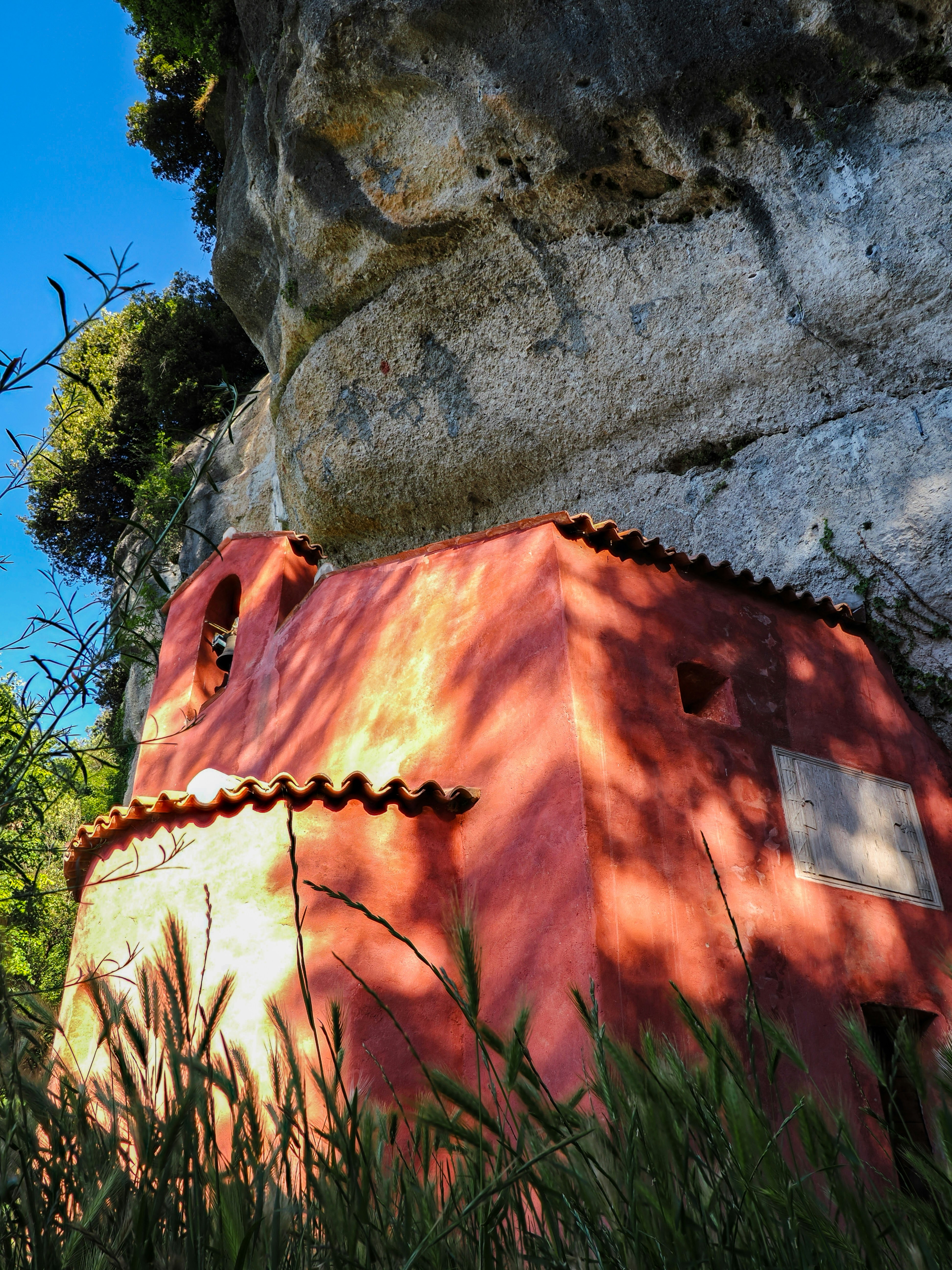 Red hillside chapel under a cliff: sunlit adobe in a rugged landscape