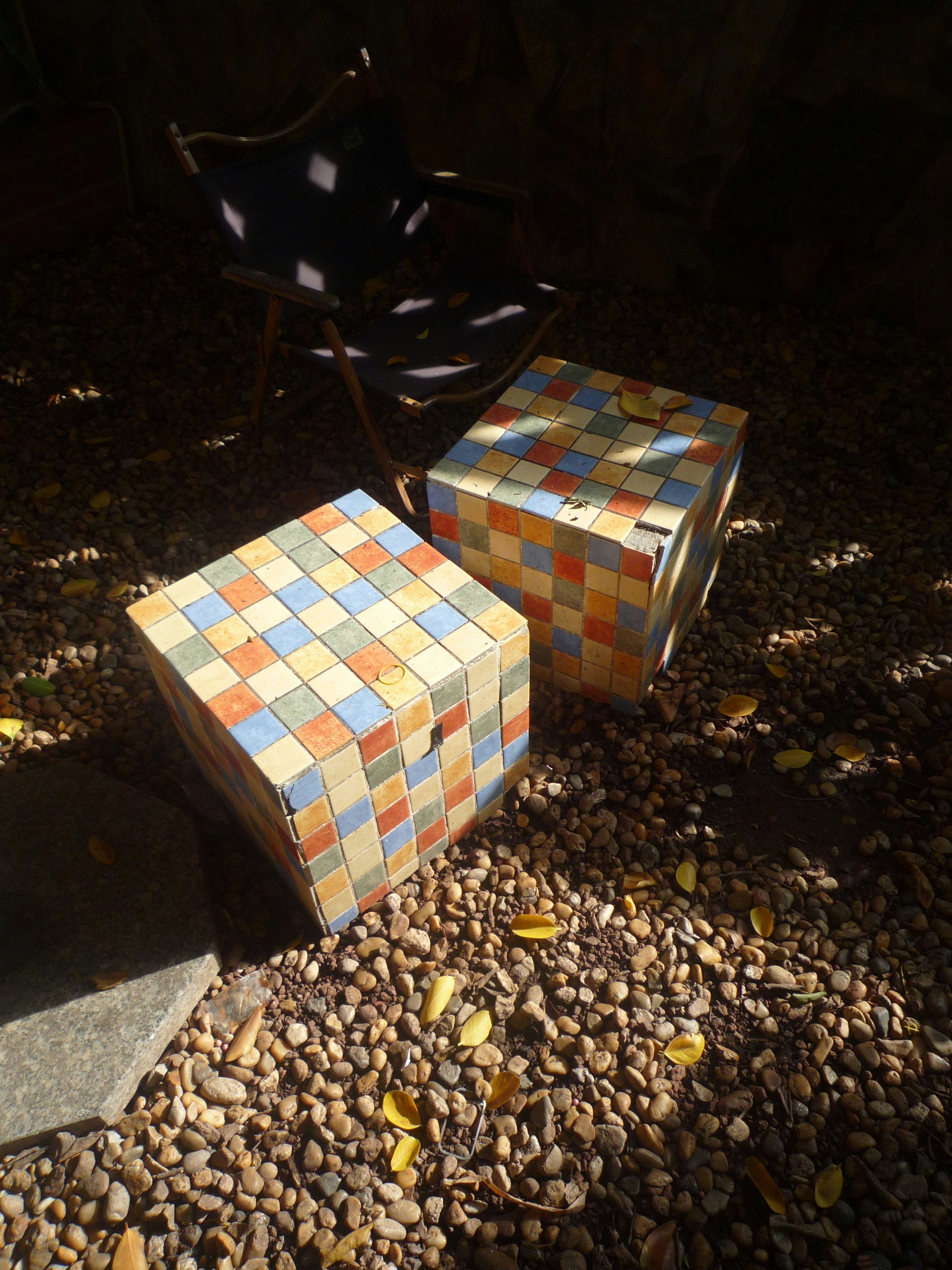 Two tiled checkered stools on gravel with a chair.