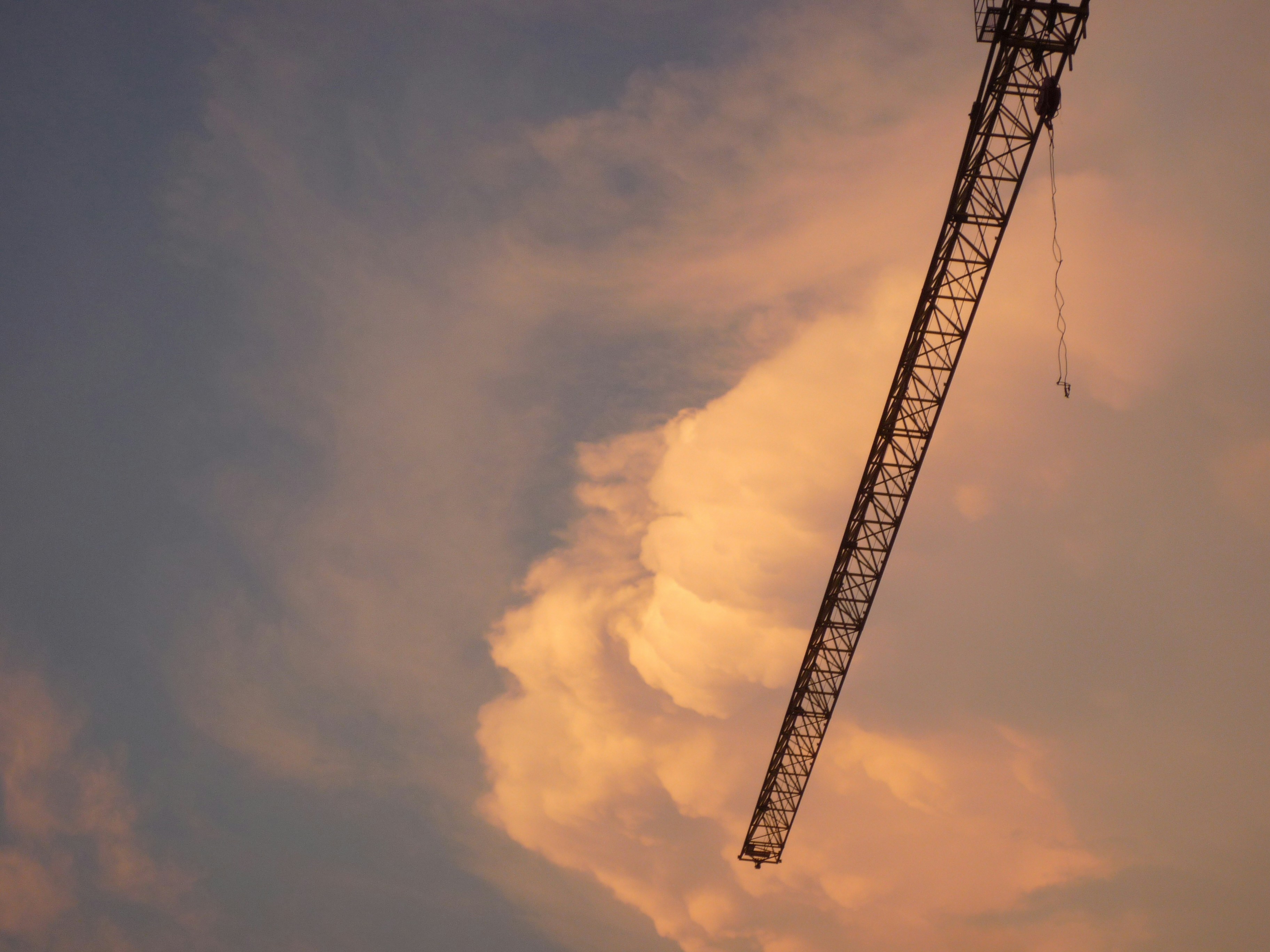 Crane silhouette diagonally crosses a warm sunset sky with wispy clouds, highlighting engineering geometry against a soft gradient horizon.