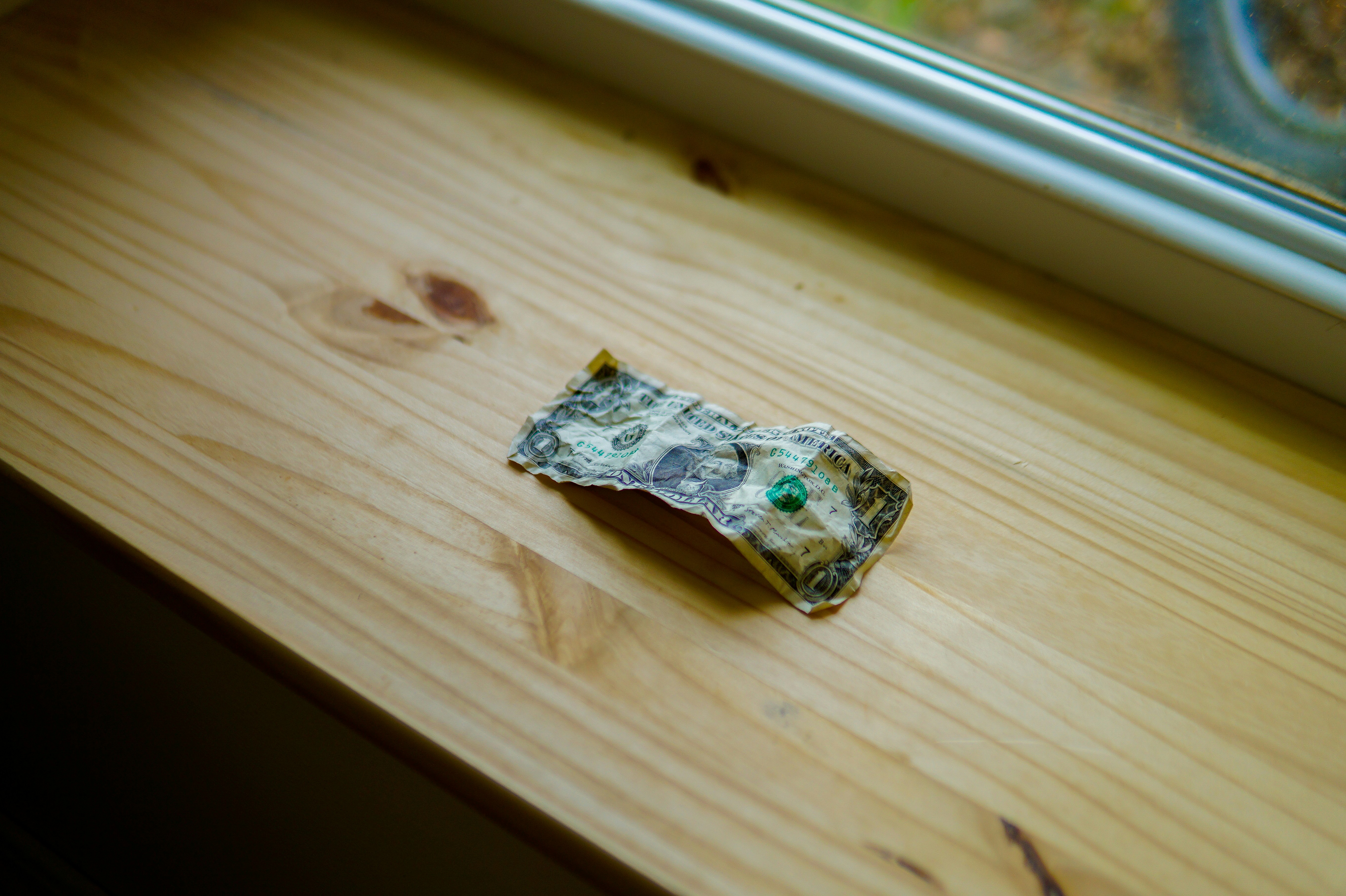A Crumpled Dollar on a Warm Wooden Window Sill
