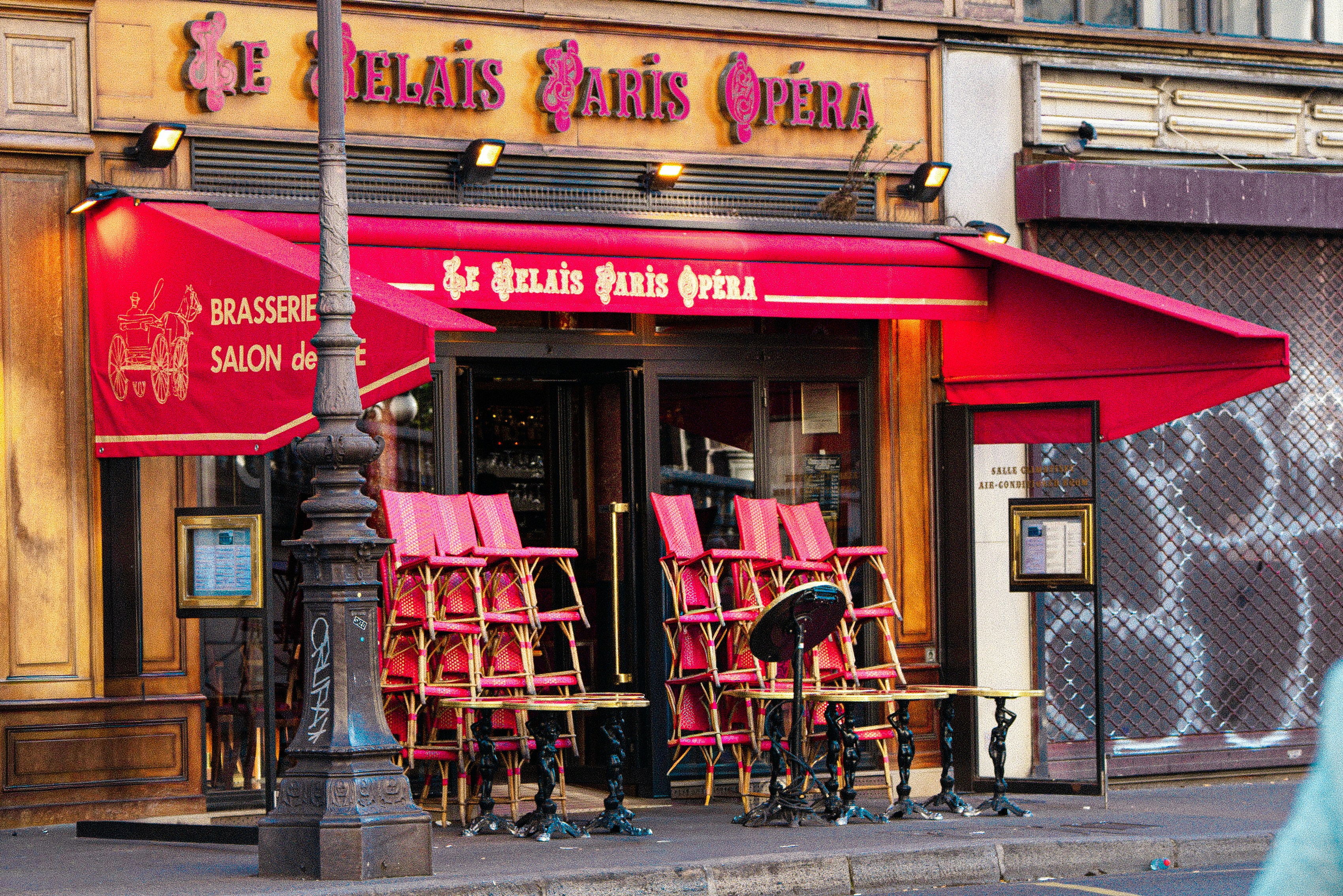 A french cafe with red awnings and stacked chairs outside.