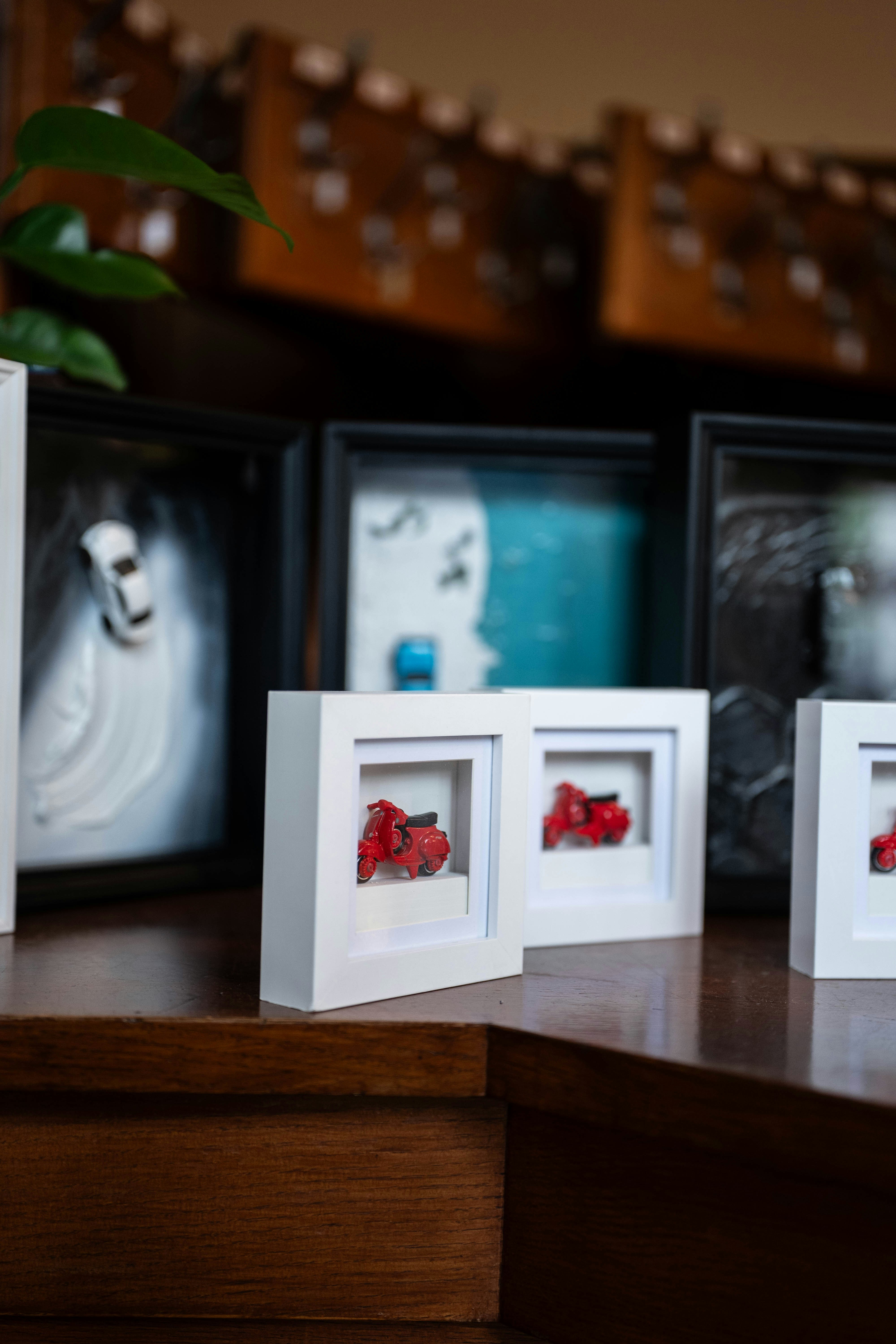Red abstract art in white frames on a wooden surface.