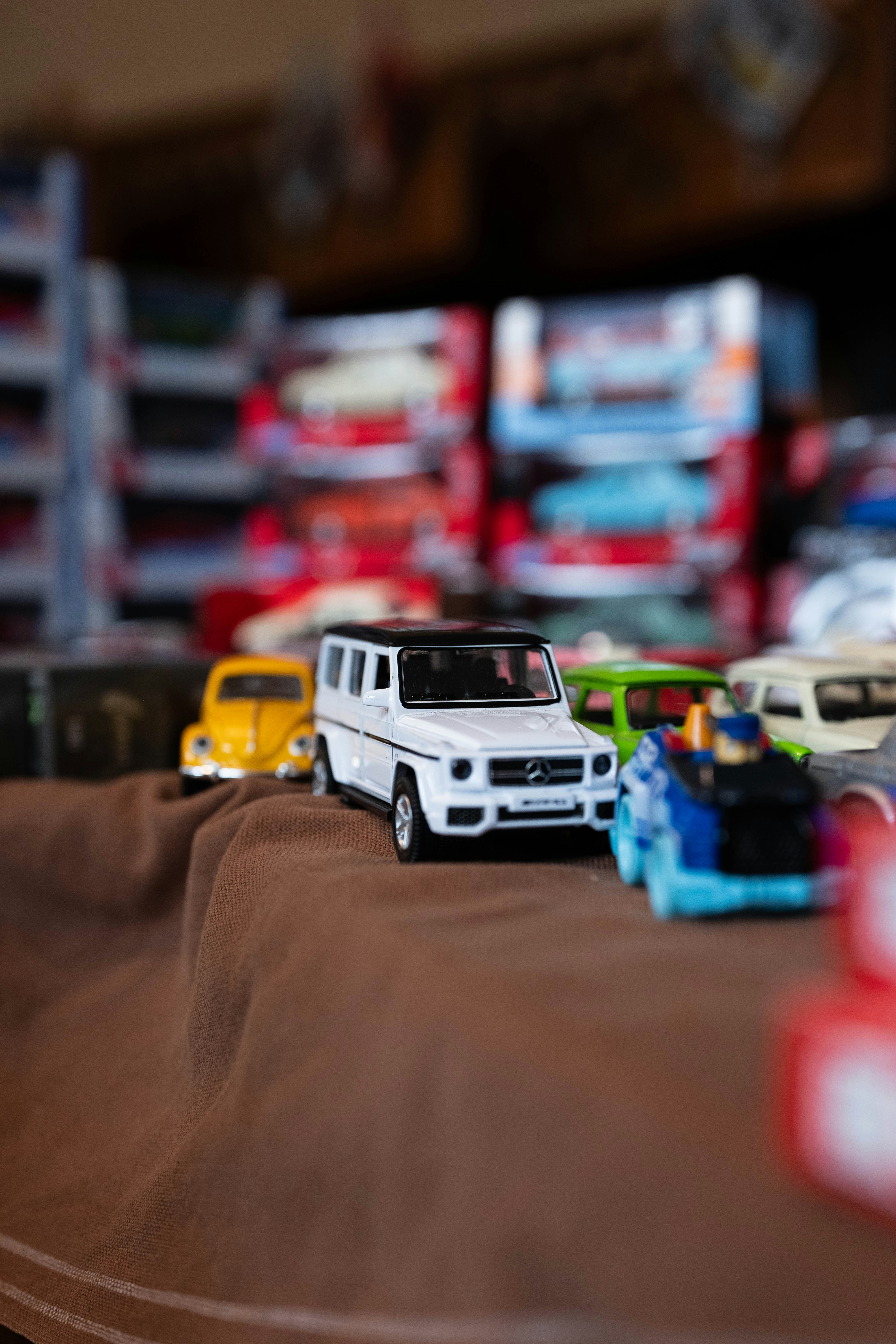 White Mercedes G-Class Toy SUV Leads a Line of Mini Vehicles on Brown Fabric Road