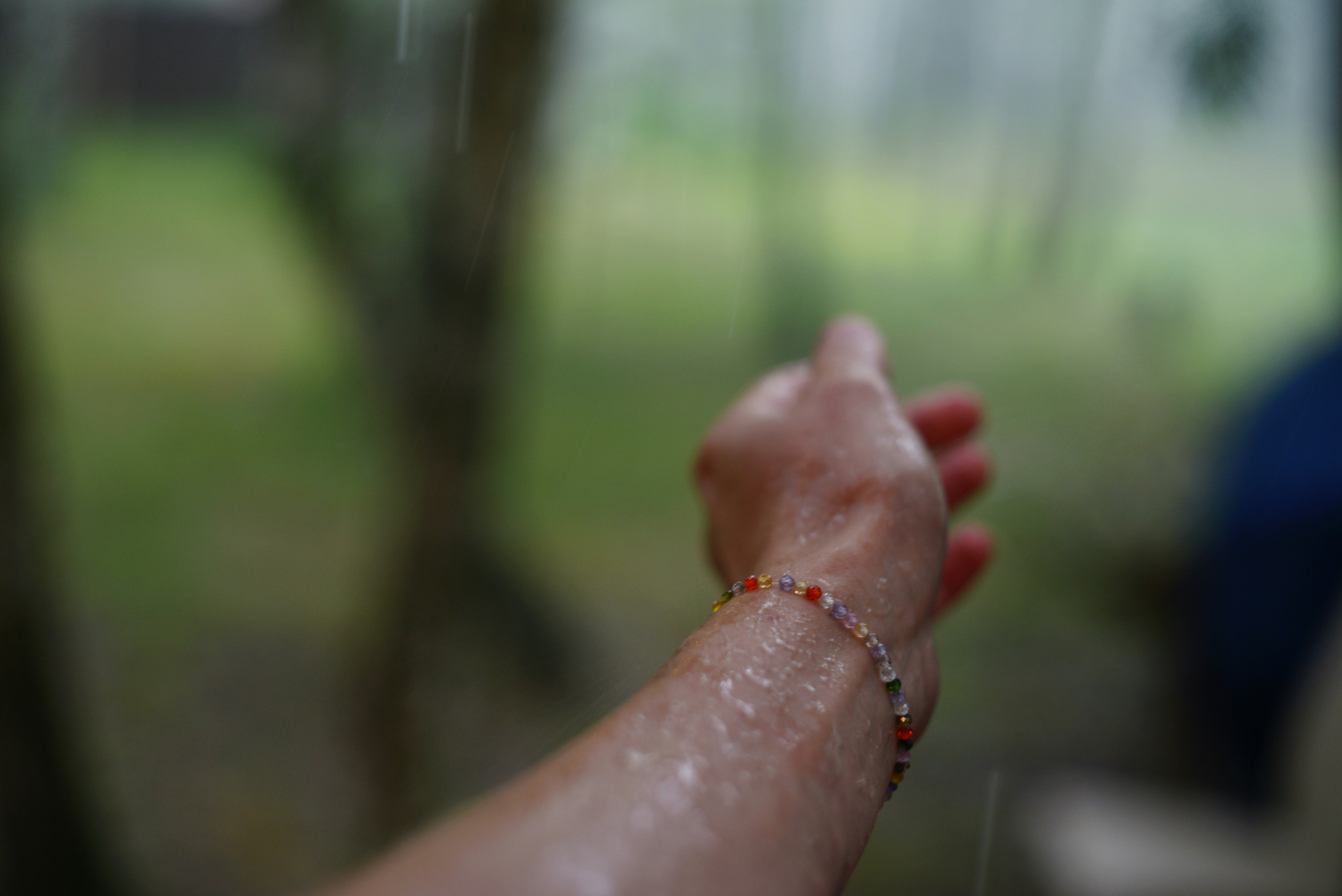 Grace in Raindrops: A Glimpse of a Braceleted Hand Reaching Through Blur