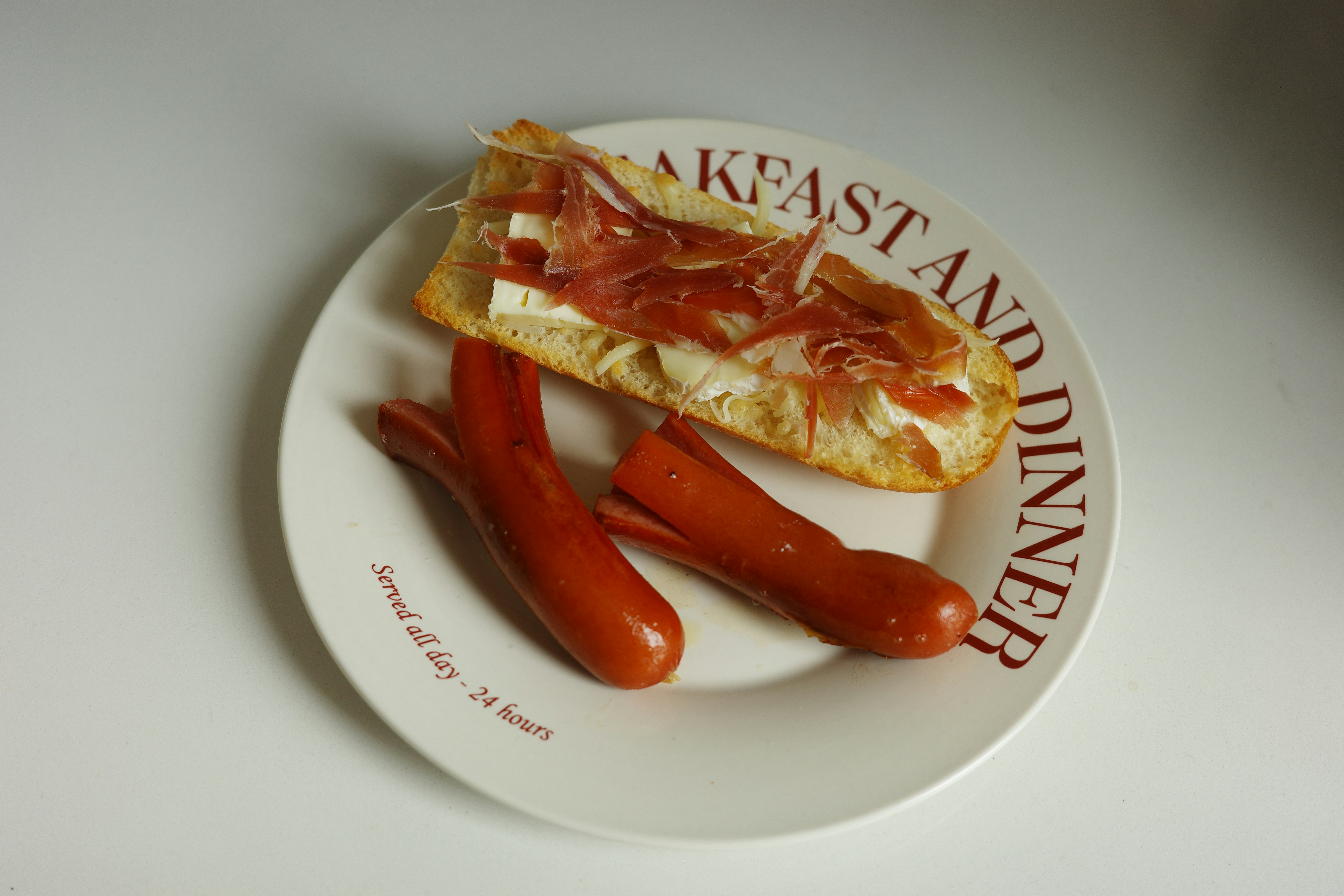 A plate with a ham sandwich and two red sausages.