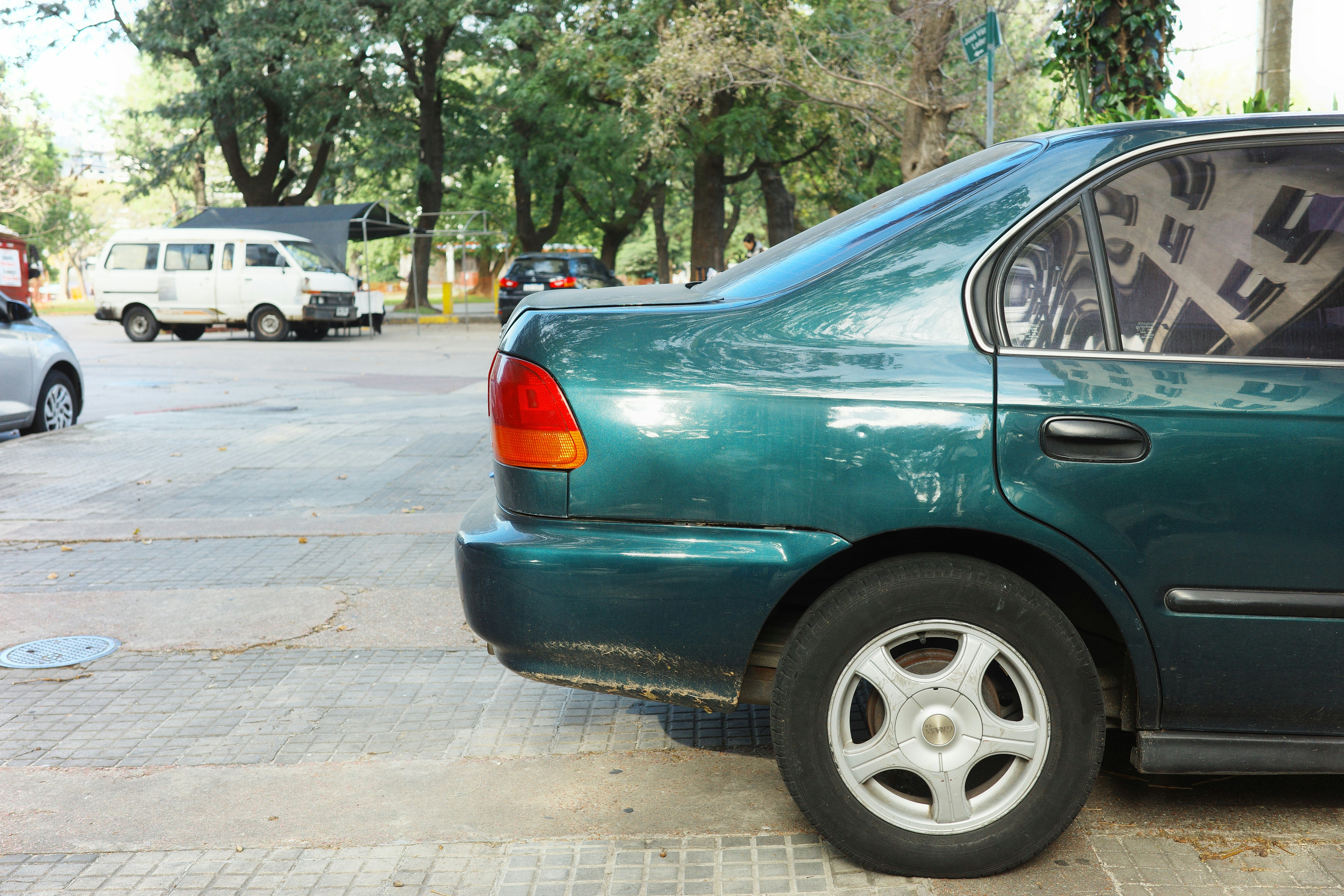 Rear-Quarter Perspective: A Dim Turquoise Sedan at the Edge of the Street