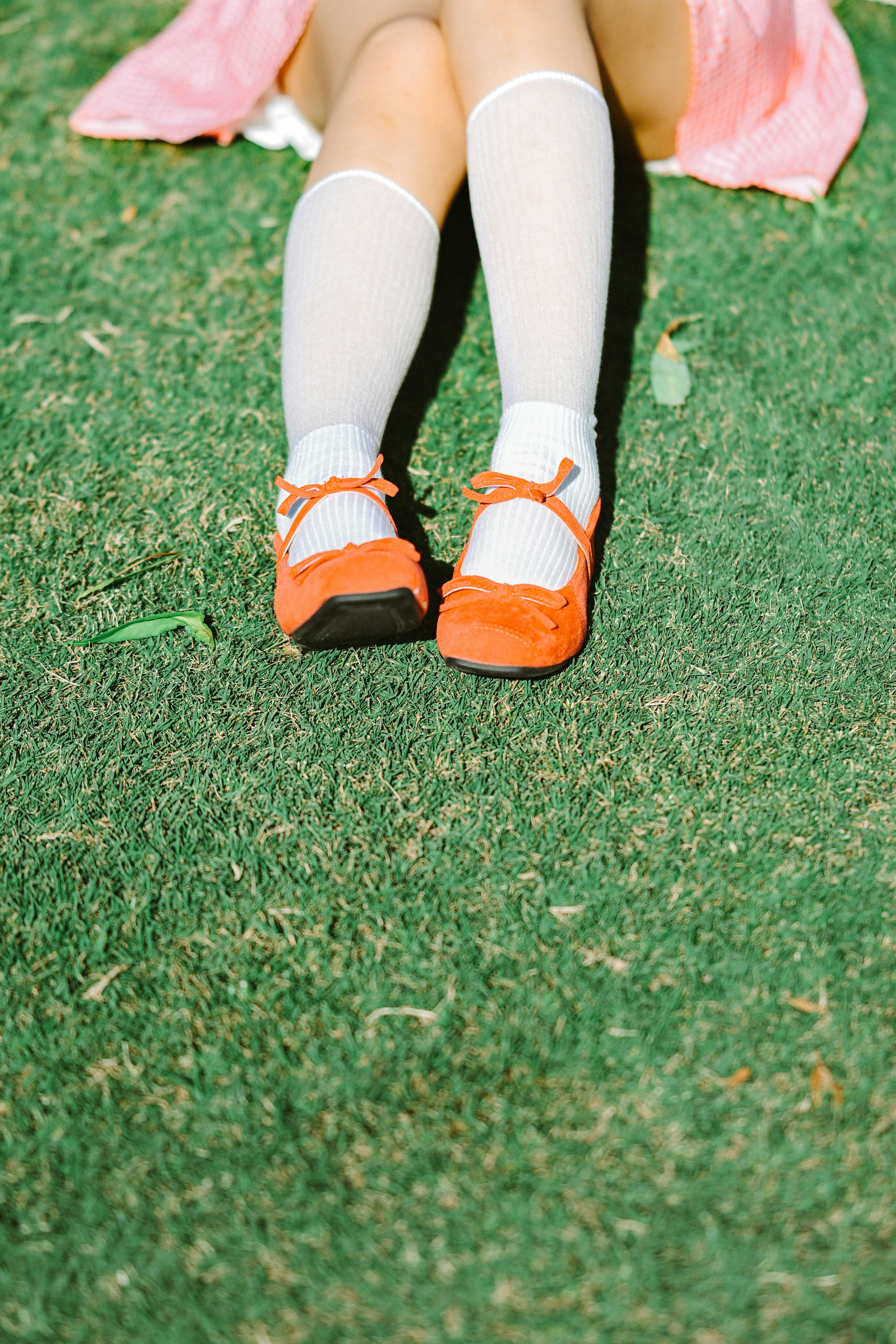 Legs with white socks and orange shoes on green grass.