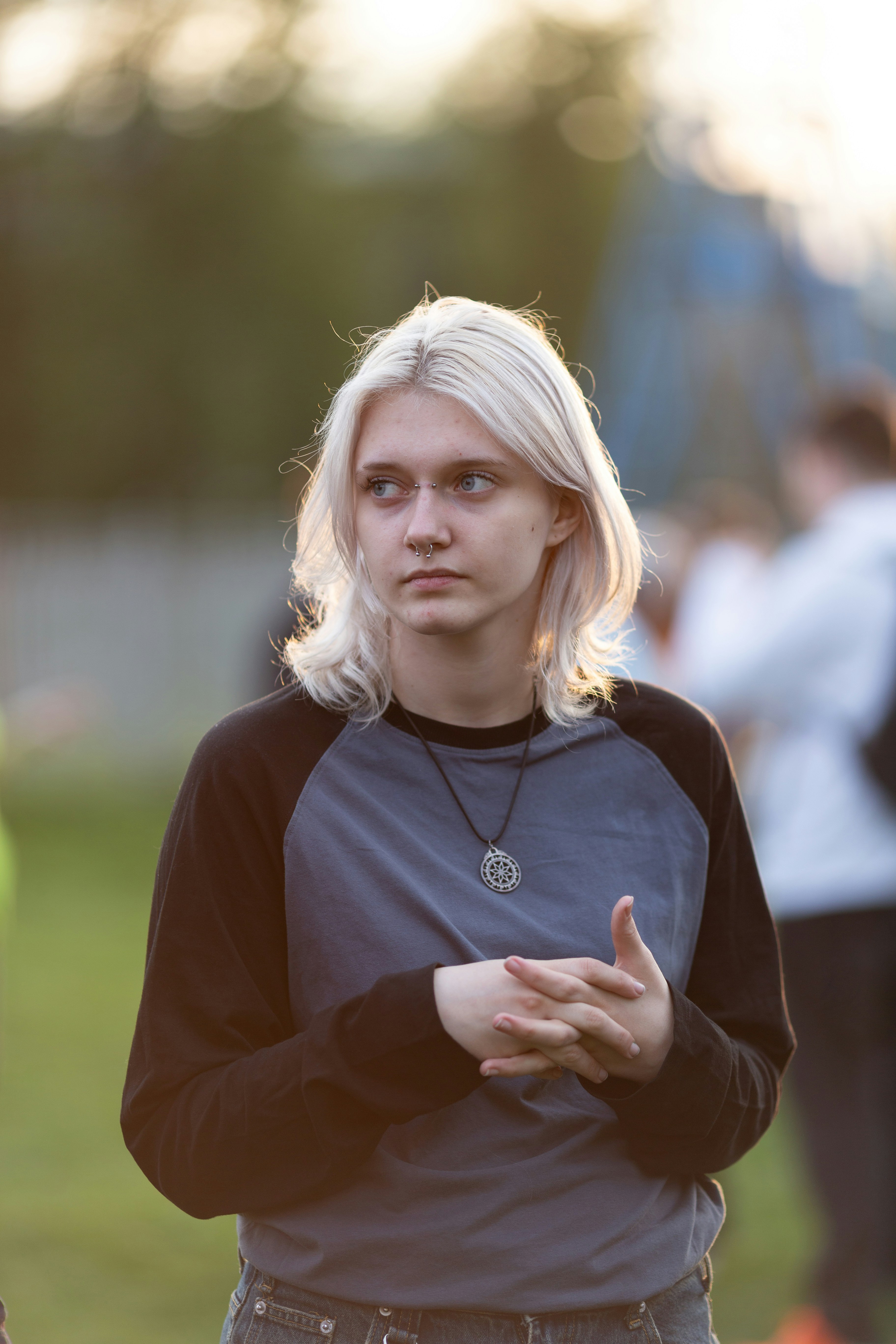  pale-haired portrait at dusk: a quiet gaze with hands folded in a sunlit field