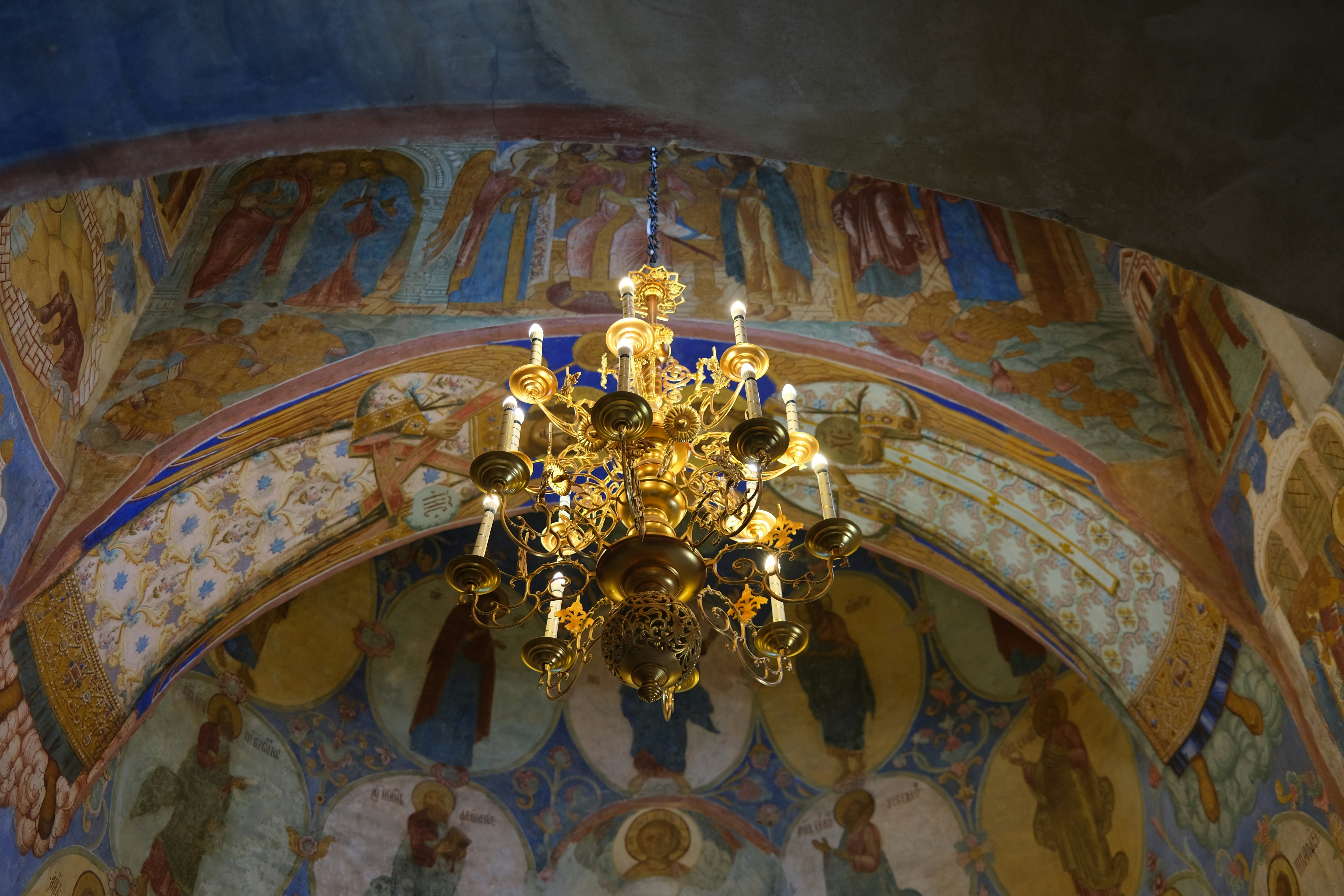 Ornate golden chandelier illuminates a frescoed church interior.