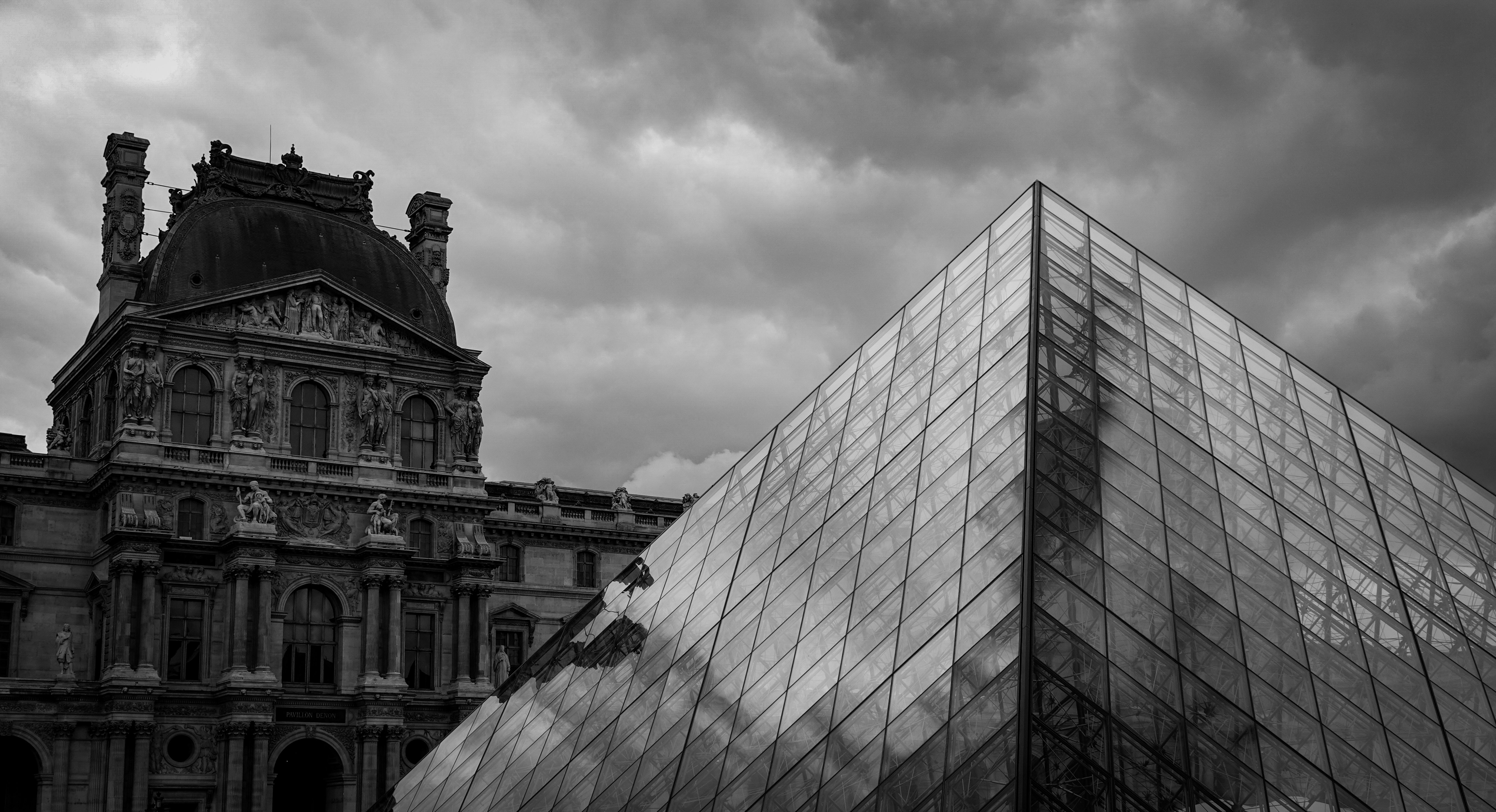 Louvre pyramid and classical building under a dramatic cloudy sky.
