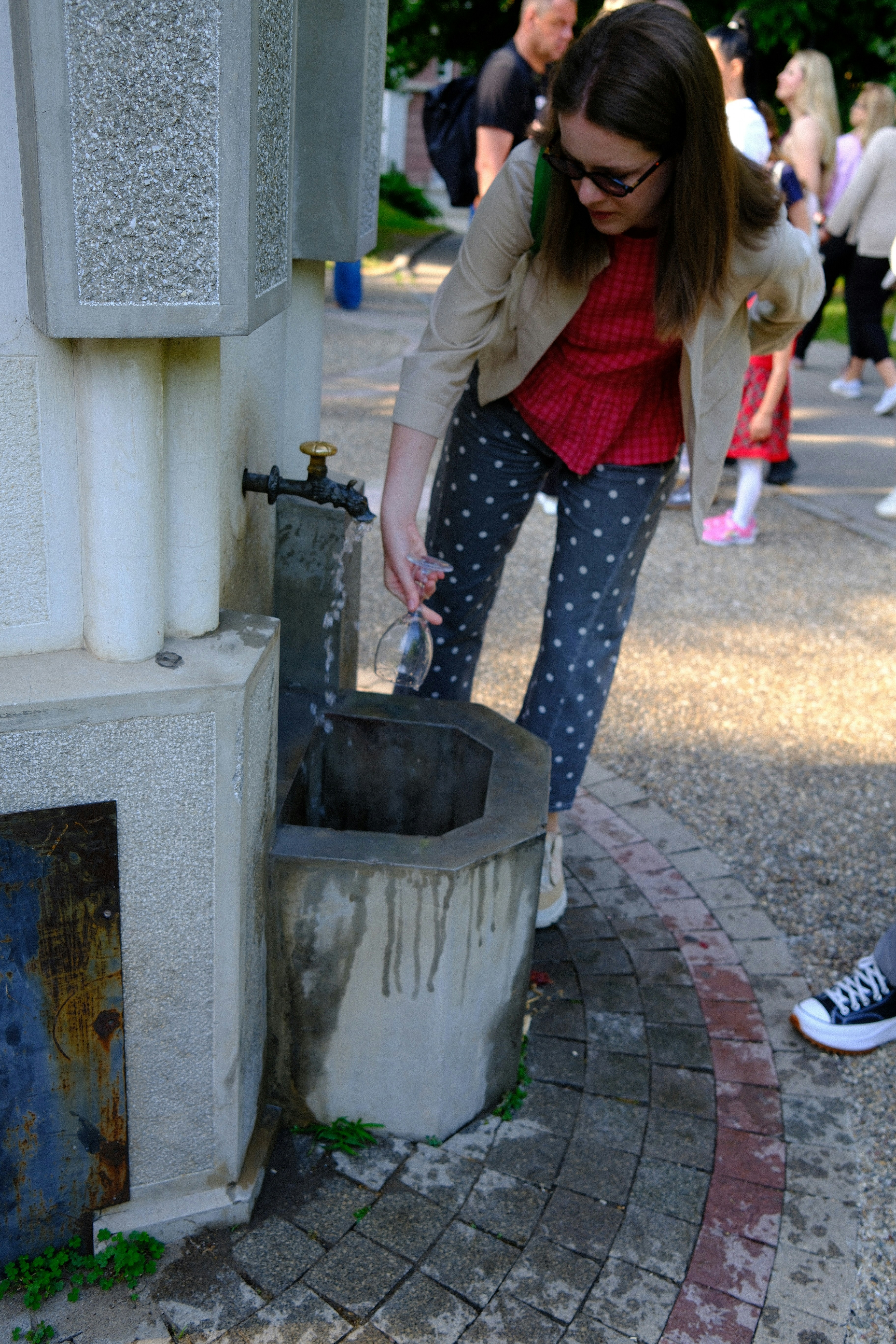 A woman fills a glass from an outdoor stone fountain.