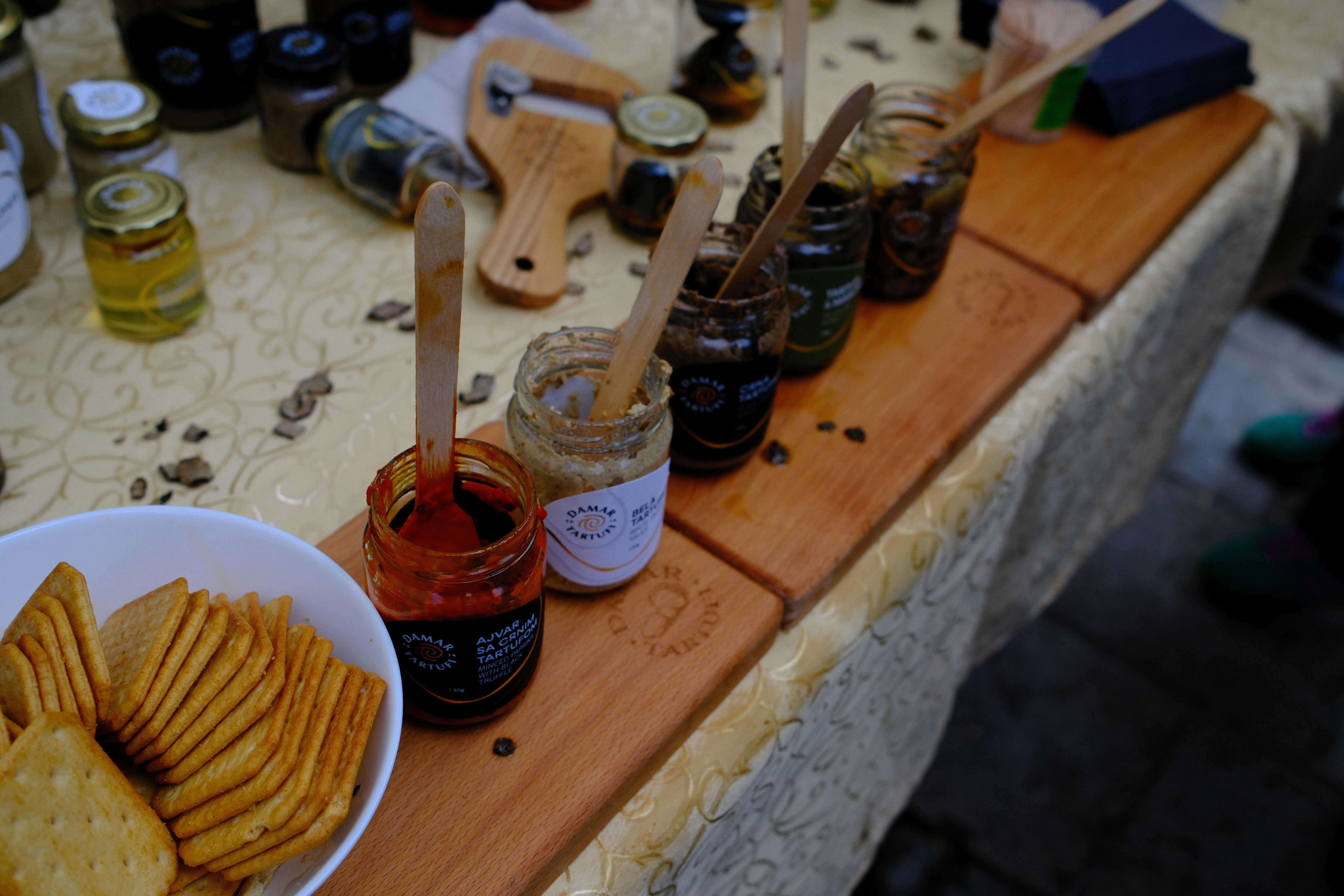 Jars of jams and spreads with crackers on a table.