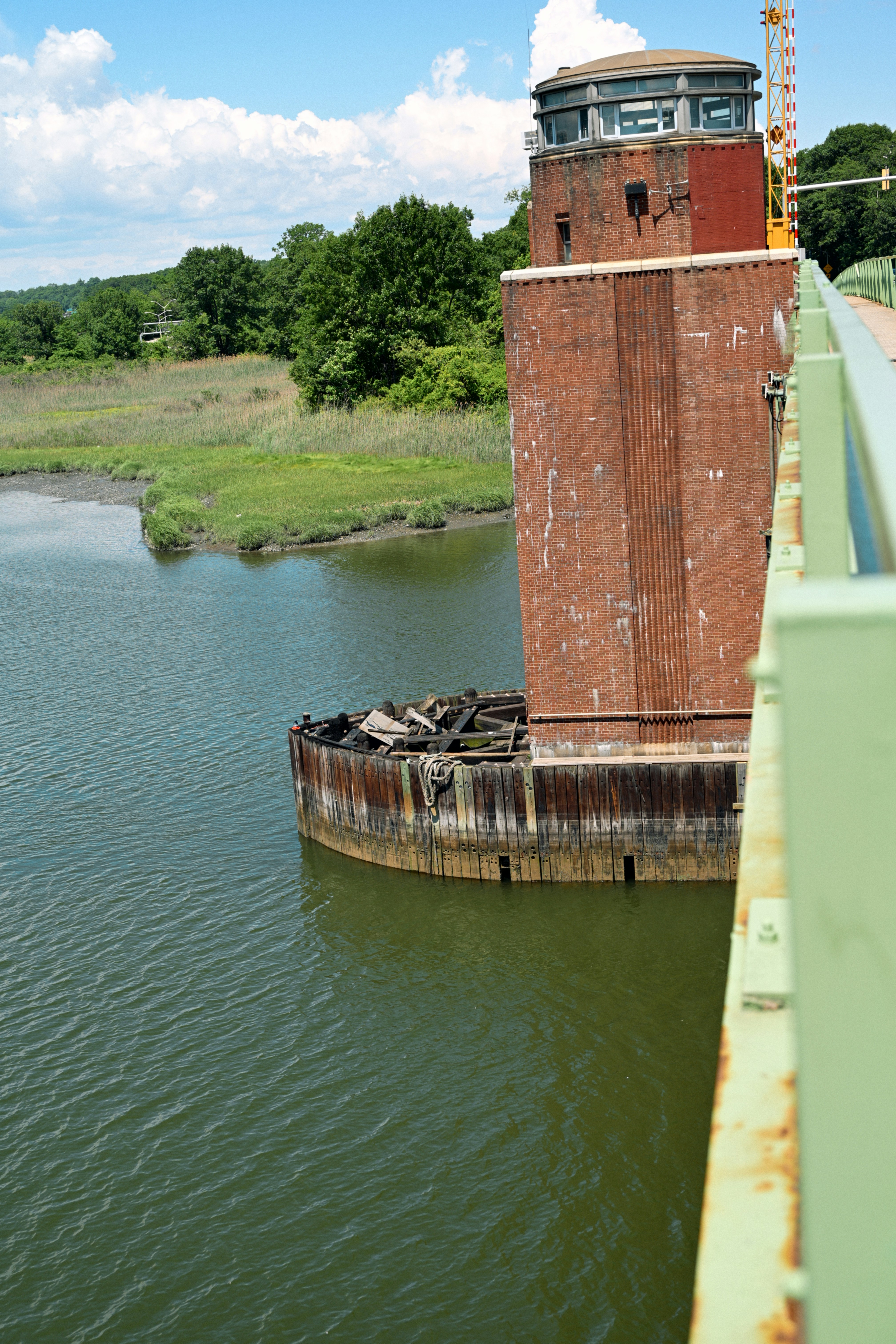 A brick tower stands beside a green river and marshland.