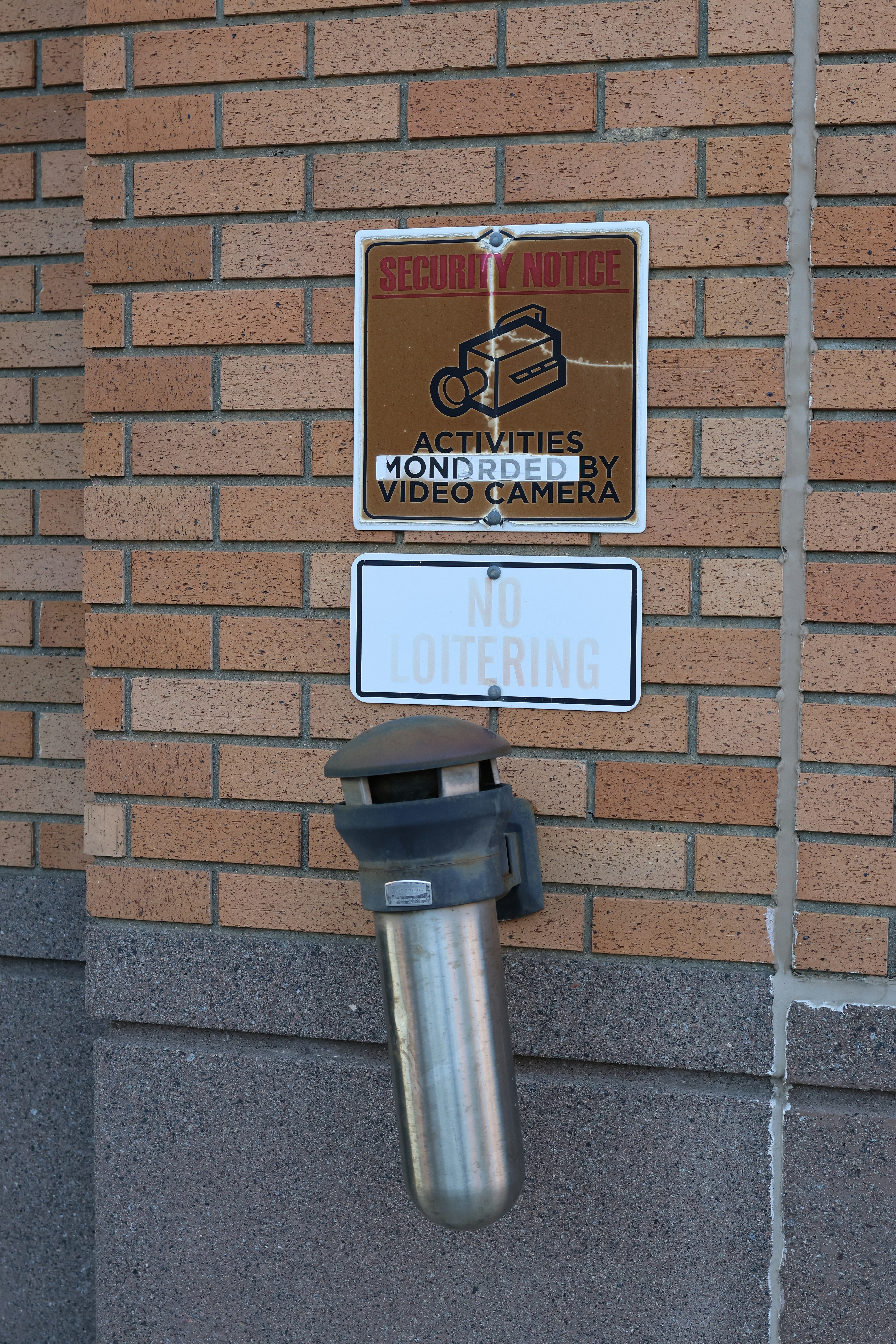 Security Signage and Contractor Pipe Fixture on Brick Wall