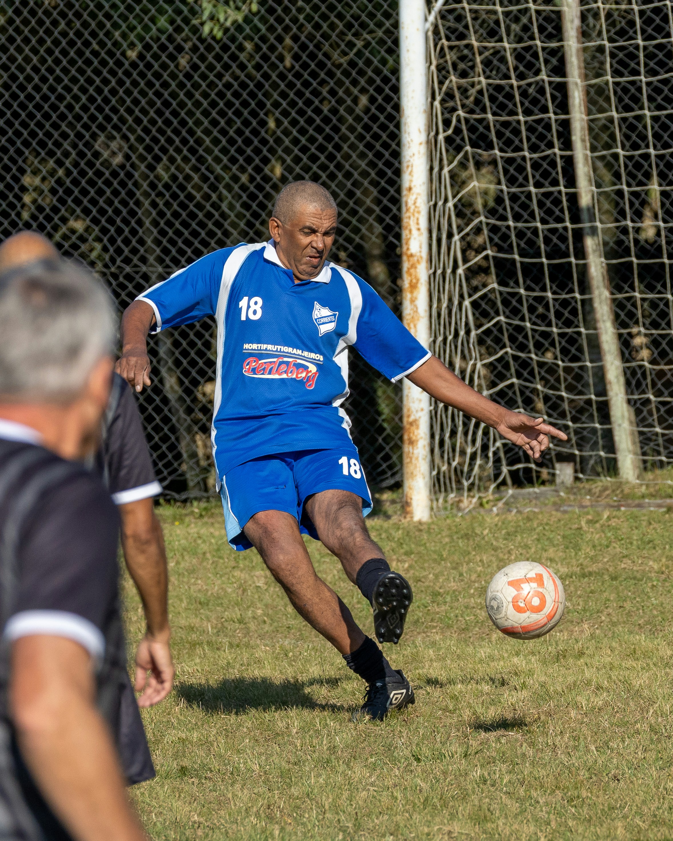 Man in blue soccer uniform kicking ball on grassy field.