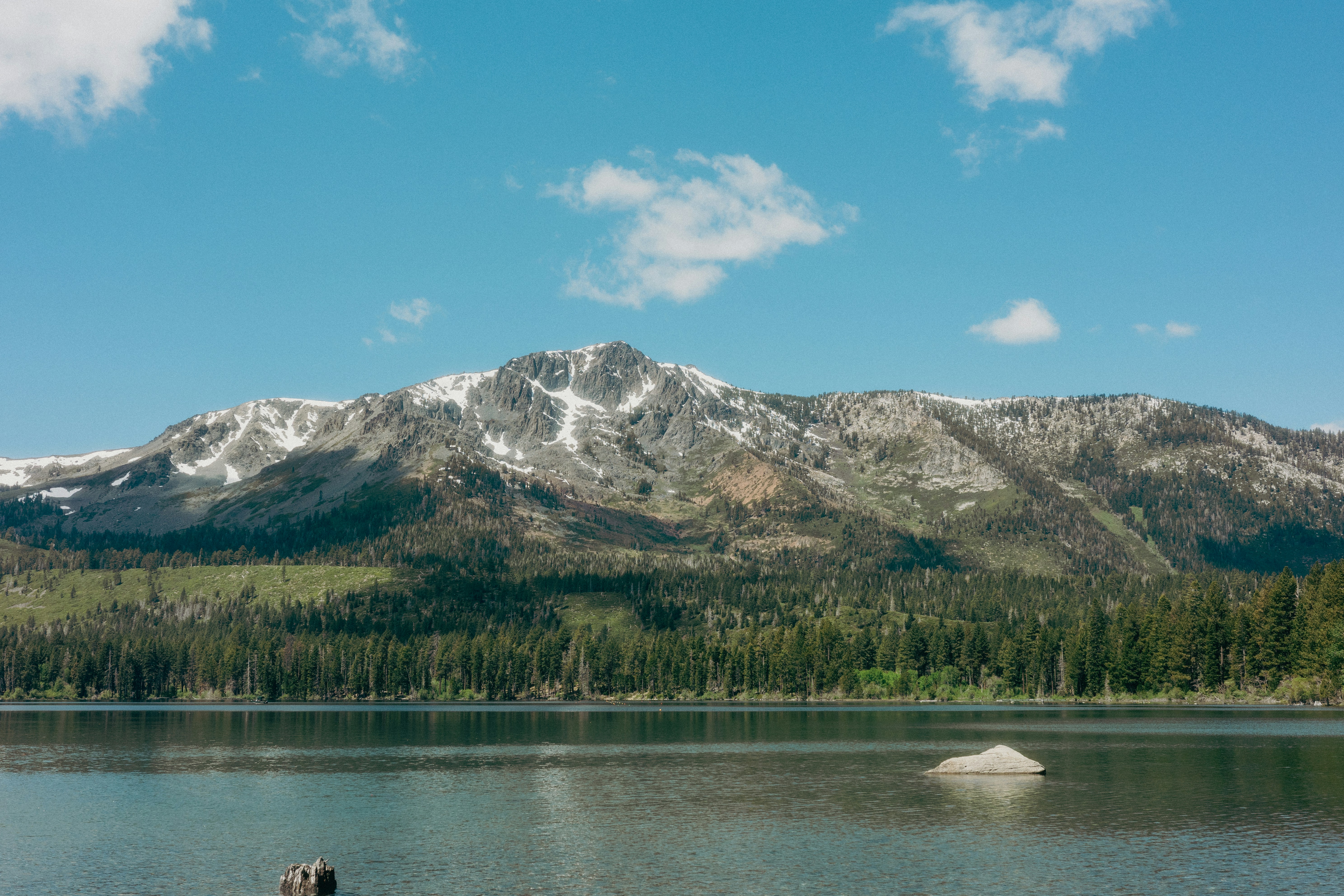 Snow-capped mountains rise above a serene lake and forest.