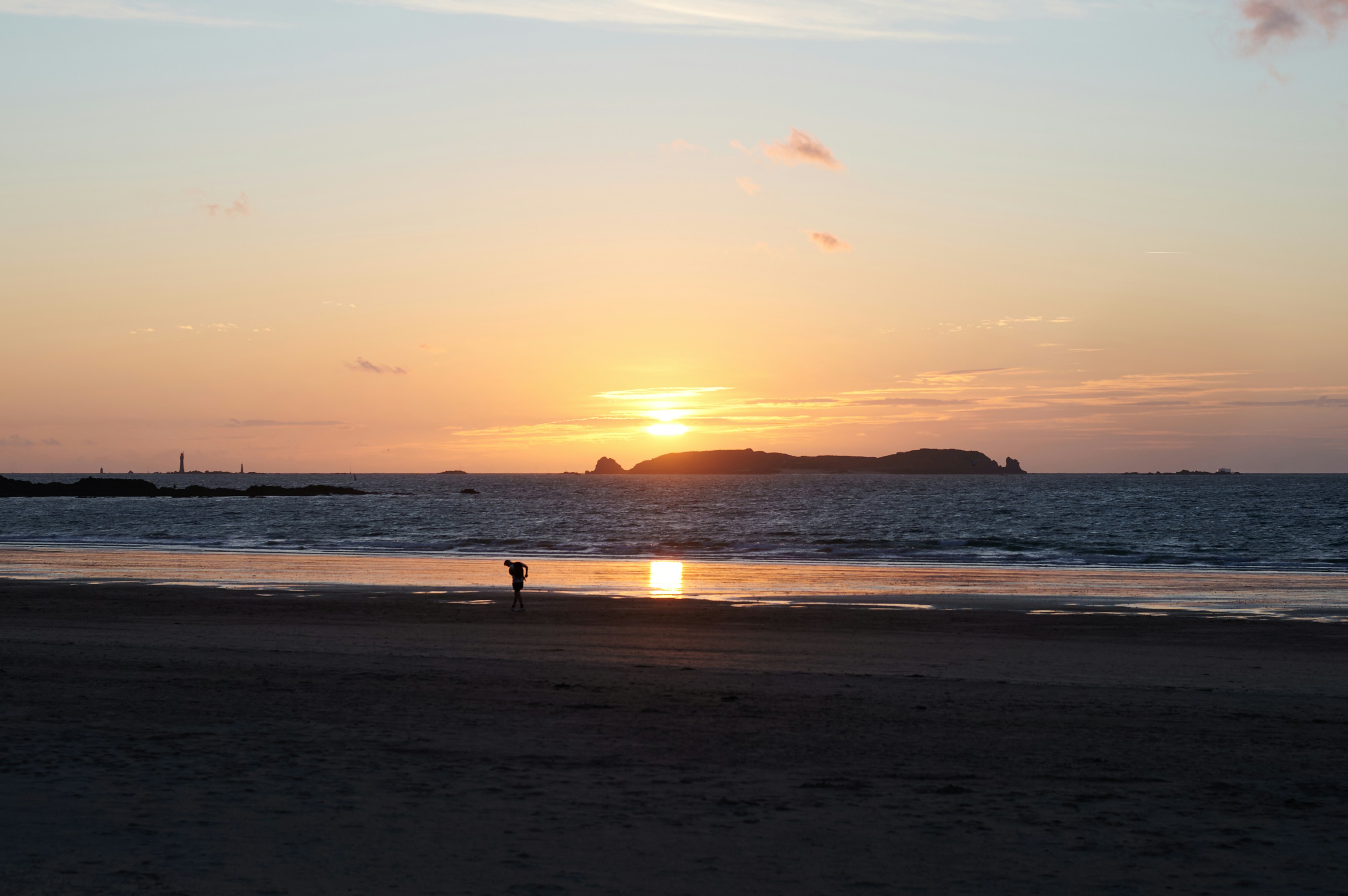 Sunset Silhouette: A lone beach figure meets the low tide against a calm horizon