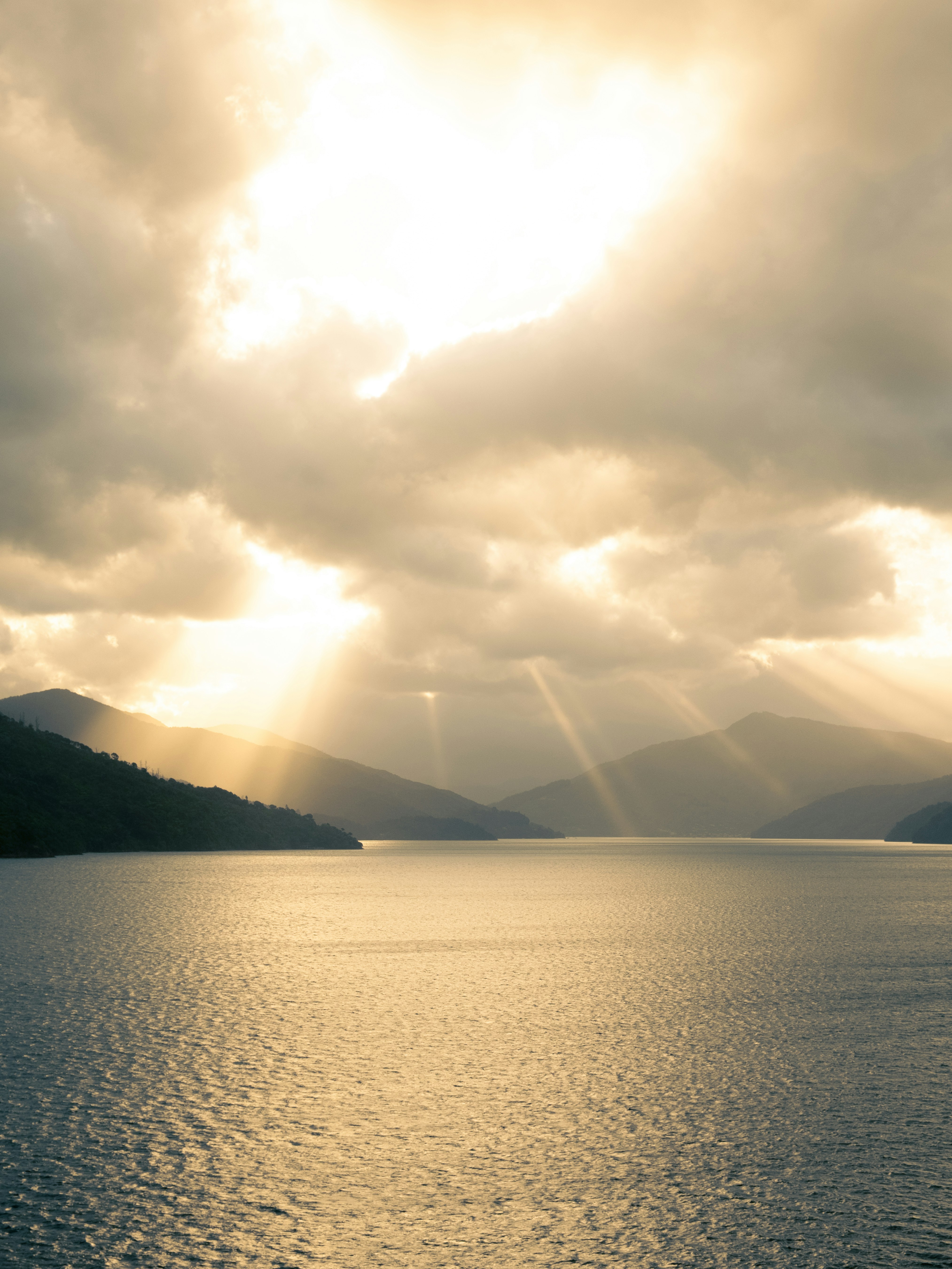 Sunbreak over tranquil fjord: a quiet embrace of light through the clouds