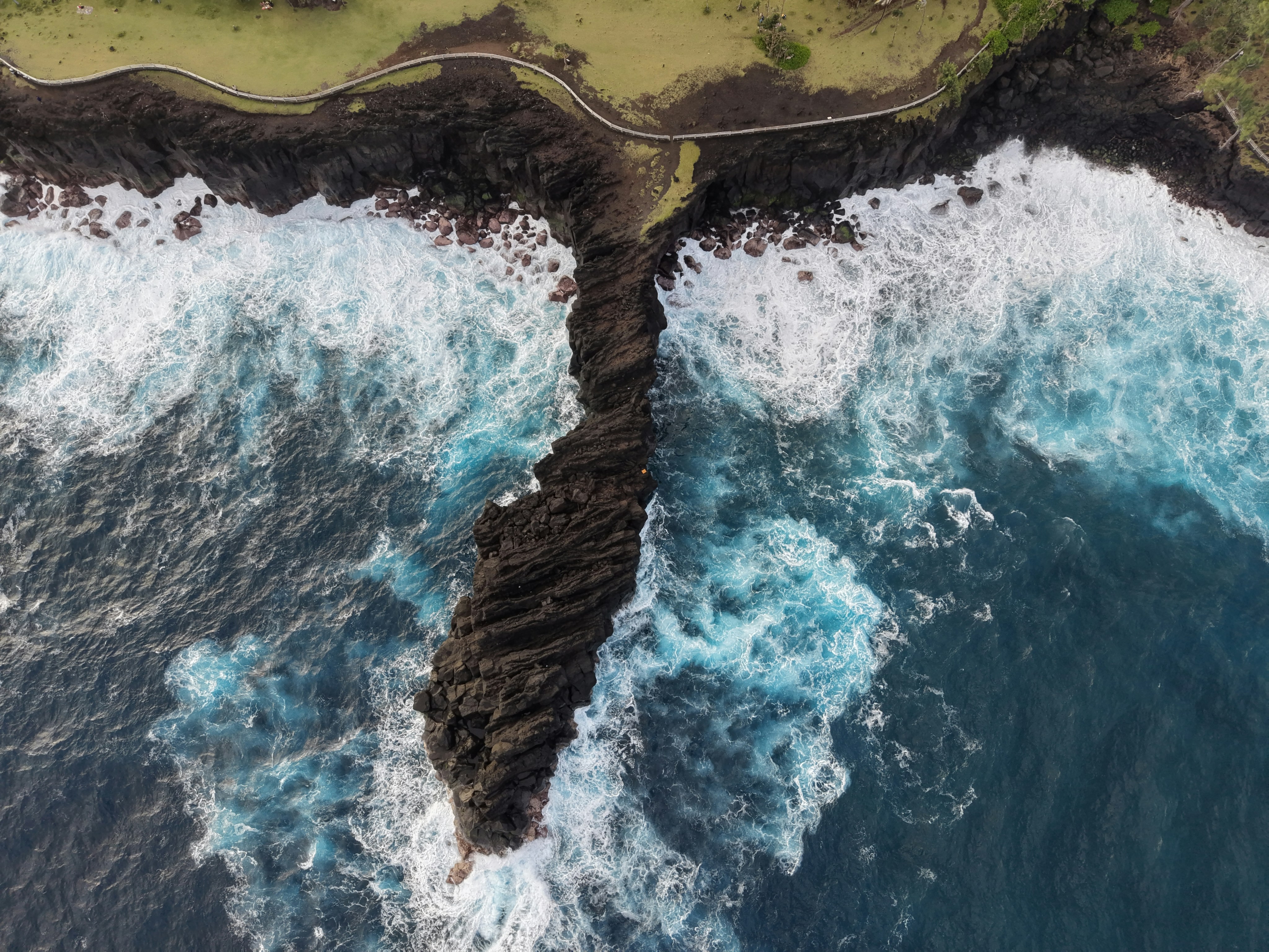 Lava-like Coastal Split: a rocky finger bisecting turquoise surf from above