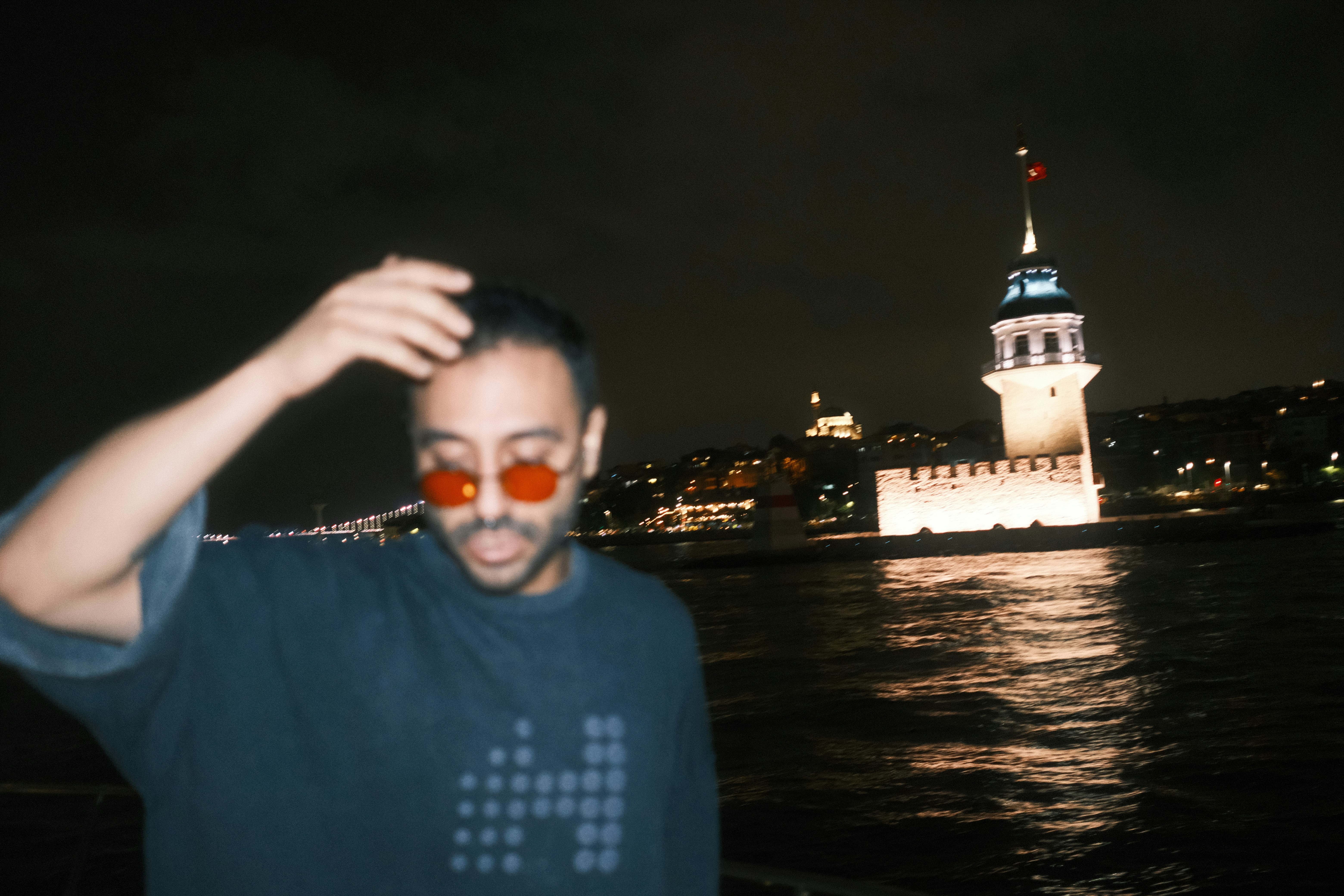 Man with red sunglasses and a lit tower at night.