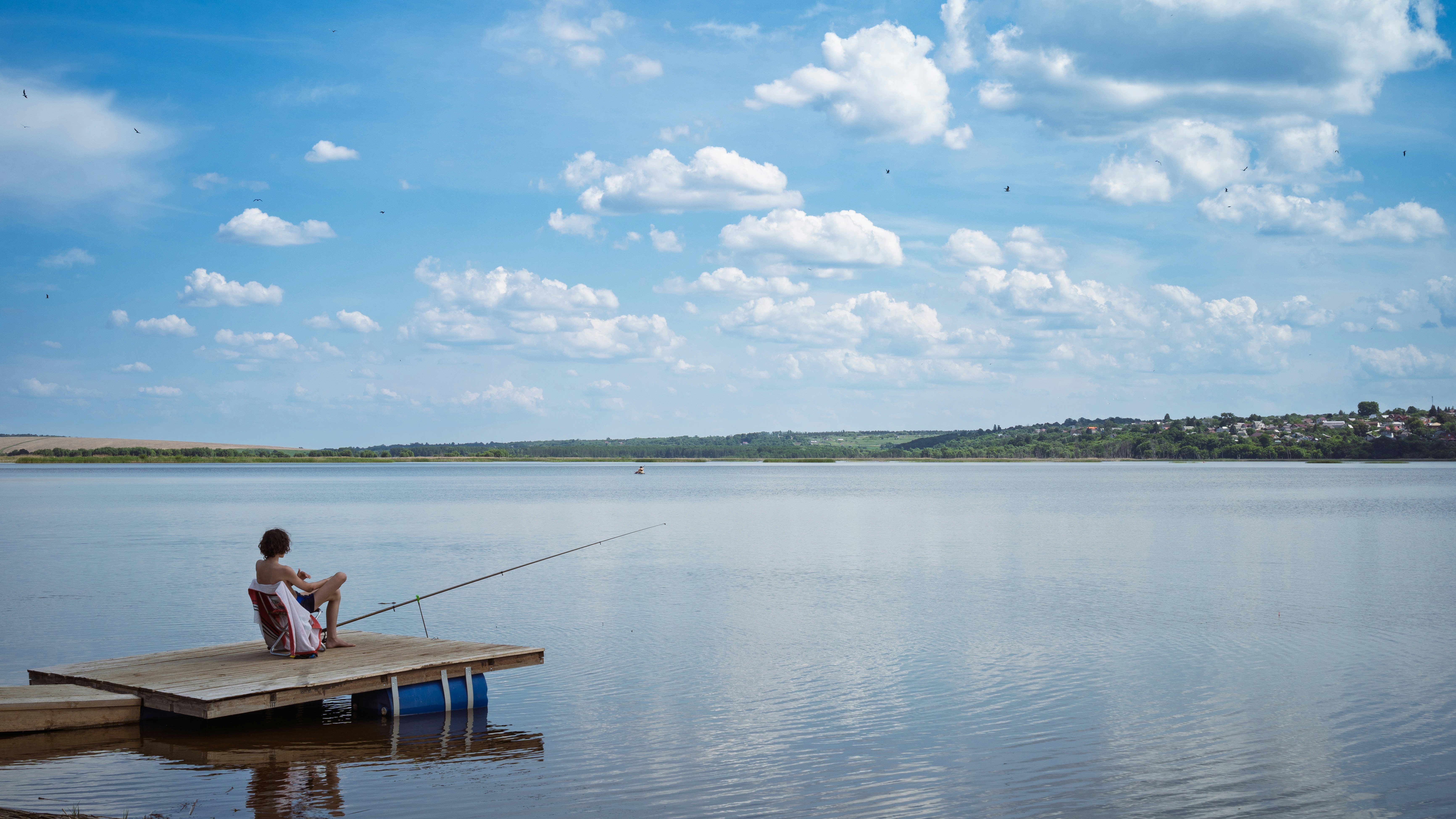 Lone person fishing on a dock in a serene lake.