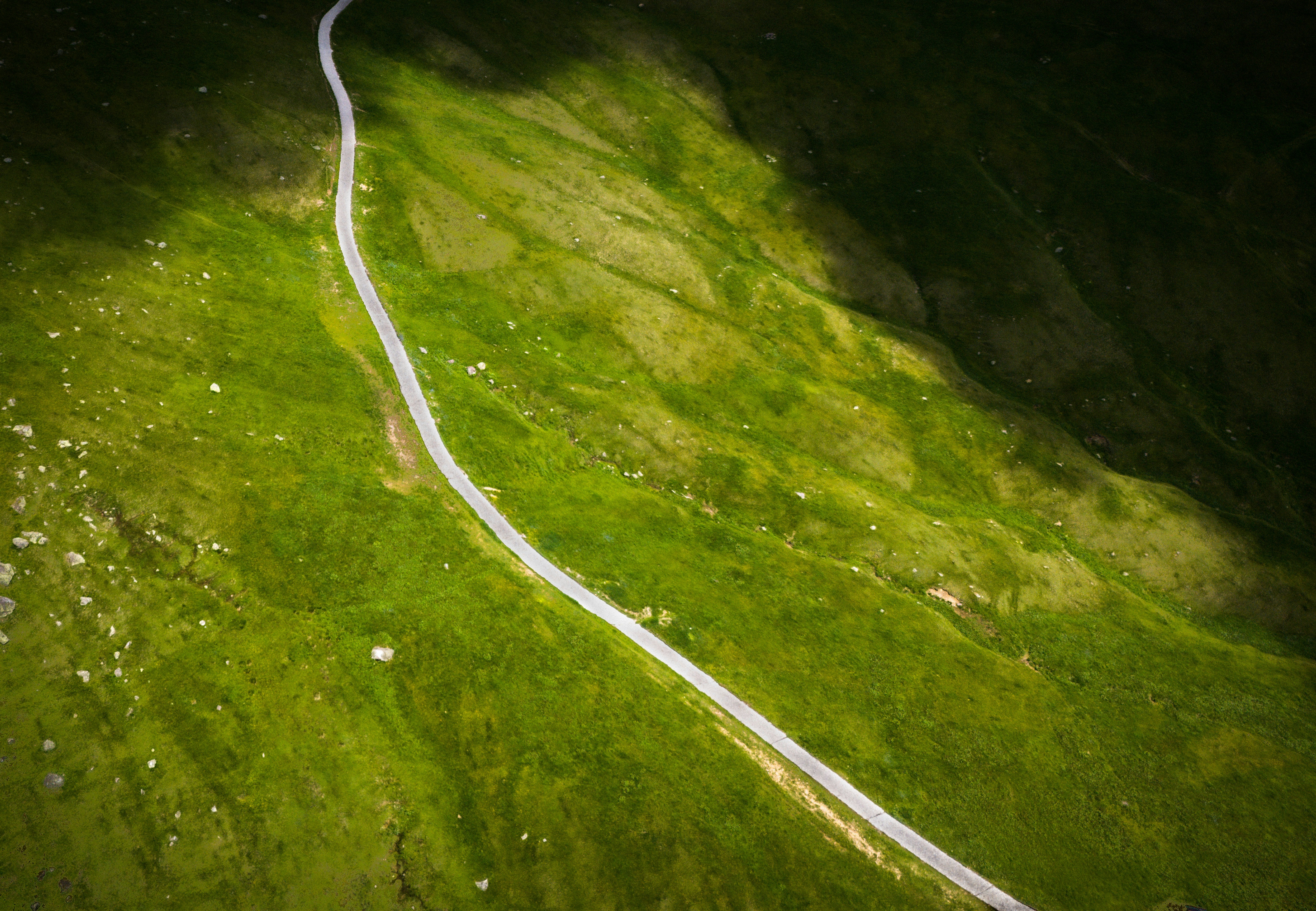 Meandering white trail through mossy emerald cliffs from above