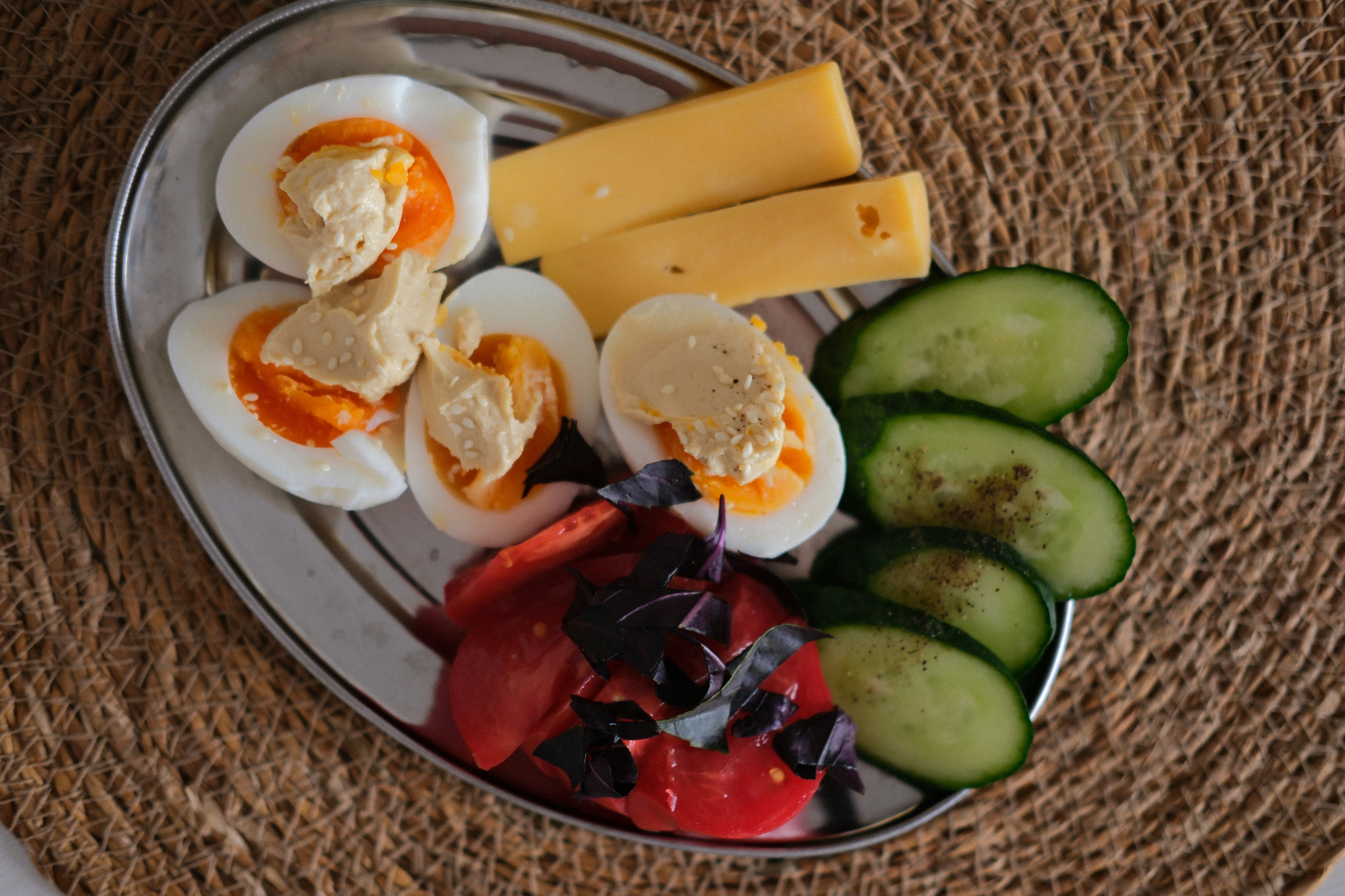 Plate of Hard-Boiled Eggs with Cheese and Veggies on a Textured Mat