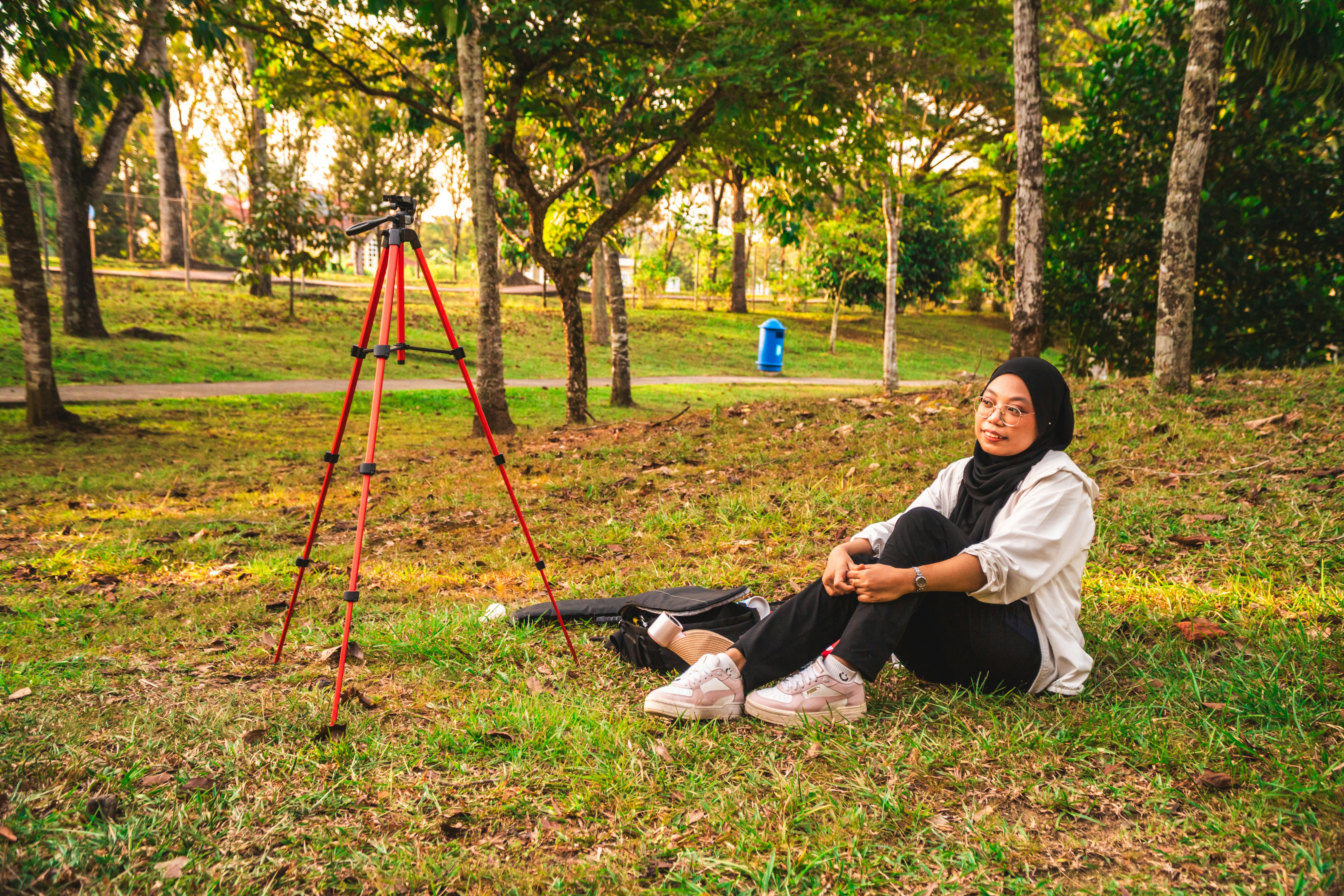 Quiet Park Portrait: A Hijab-Clad Creator Pauses beside a Red Tripod