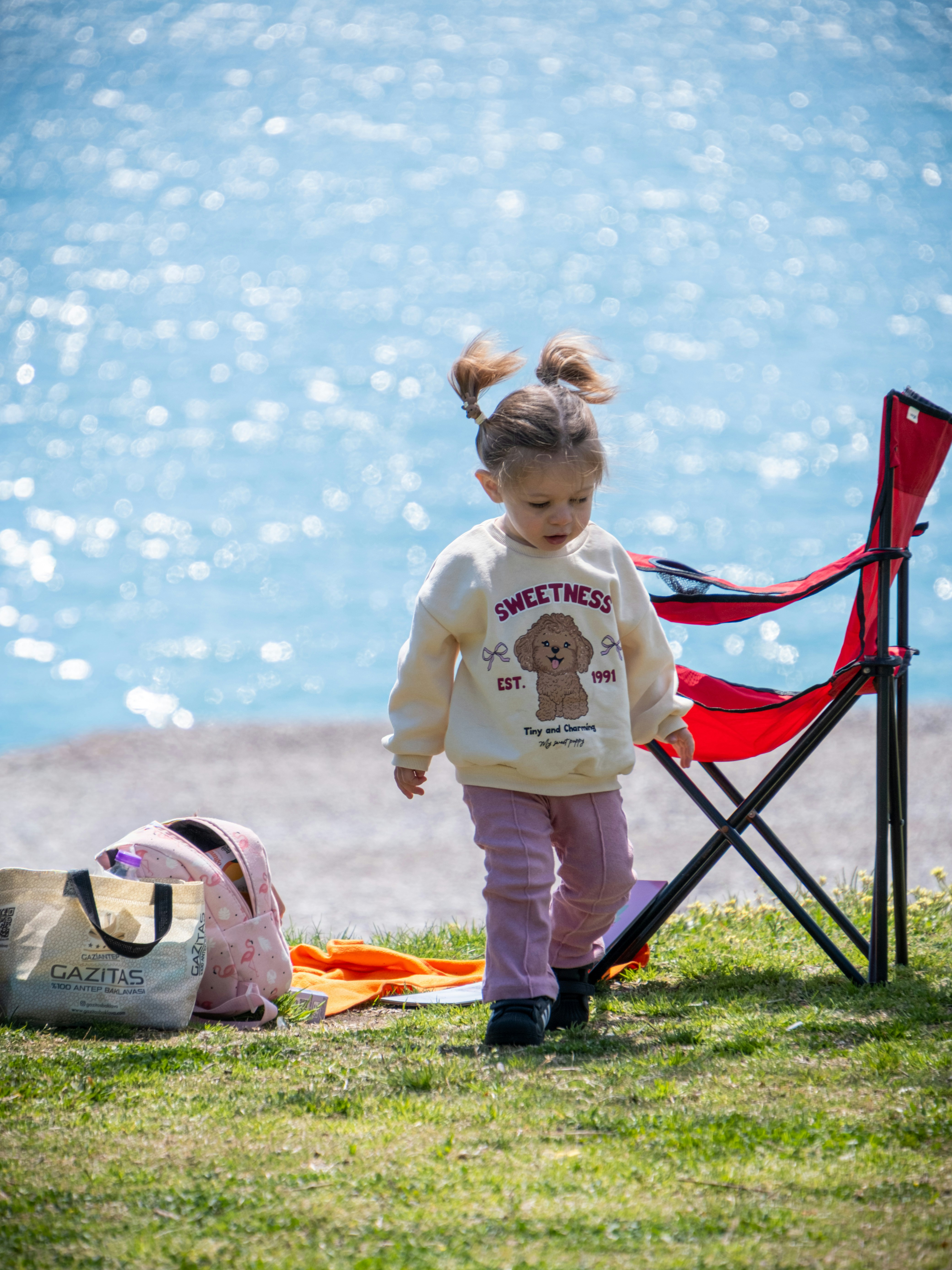 A young child walks on grass near sparkling water.