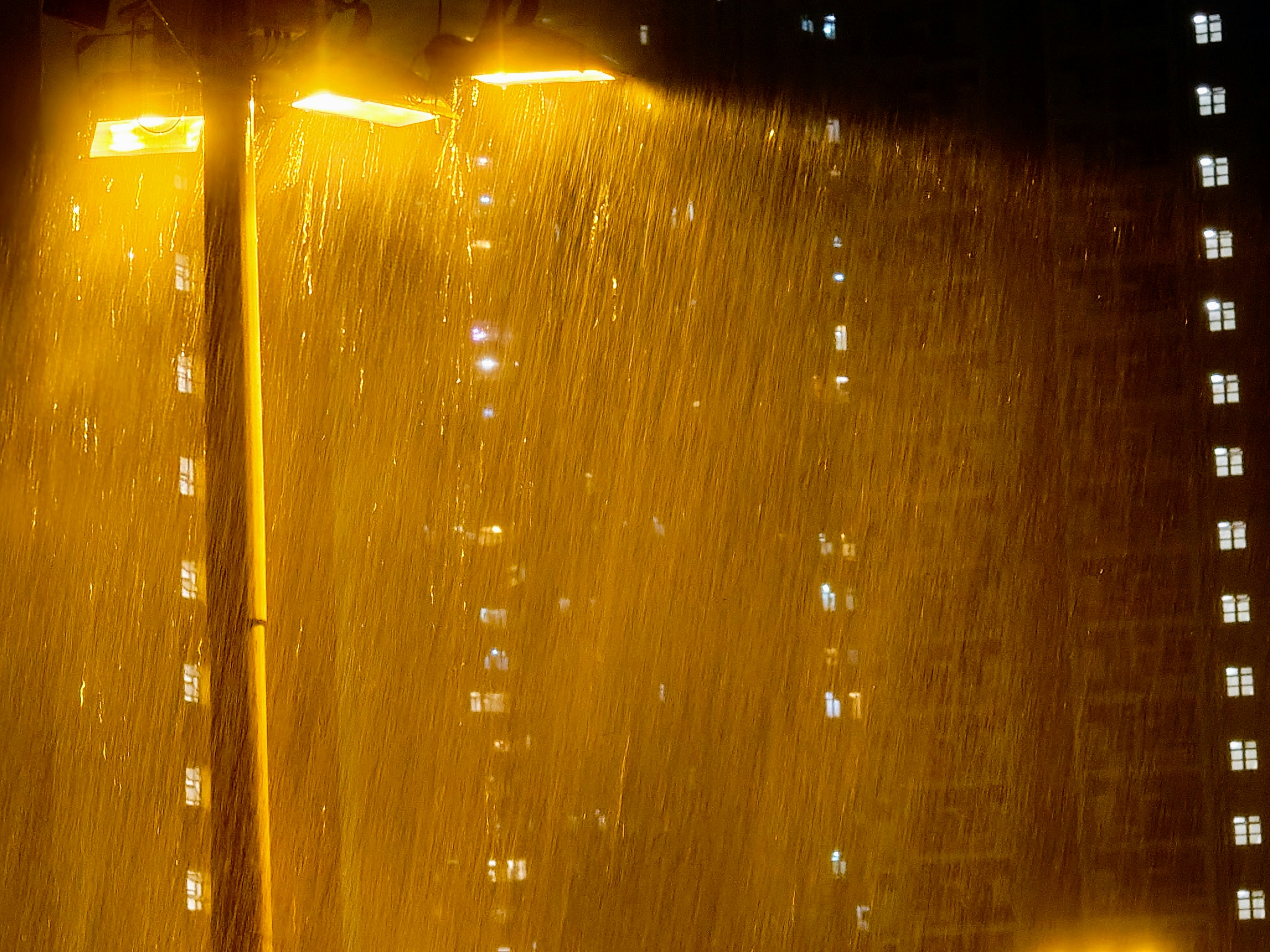 Streetlights illuminate heavy rain against a dark building at night.